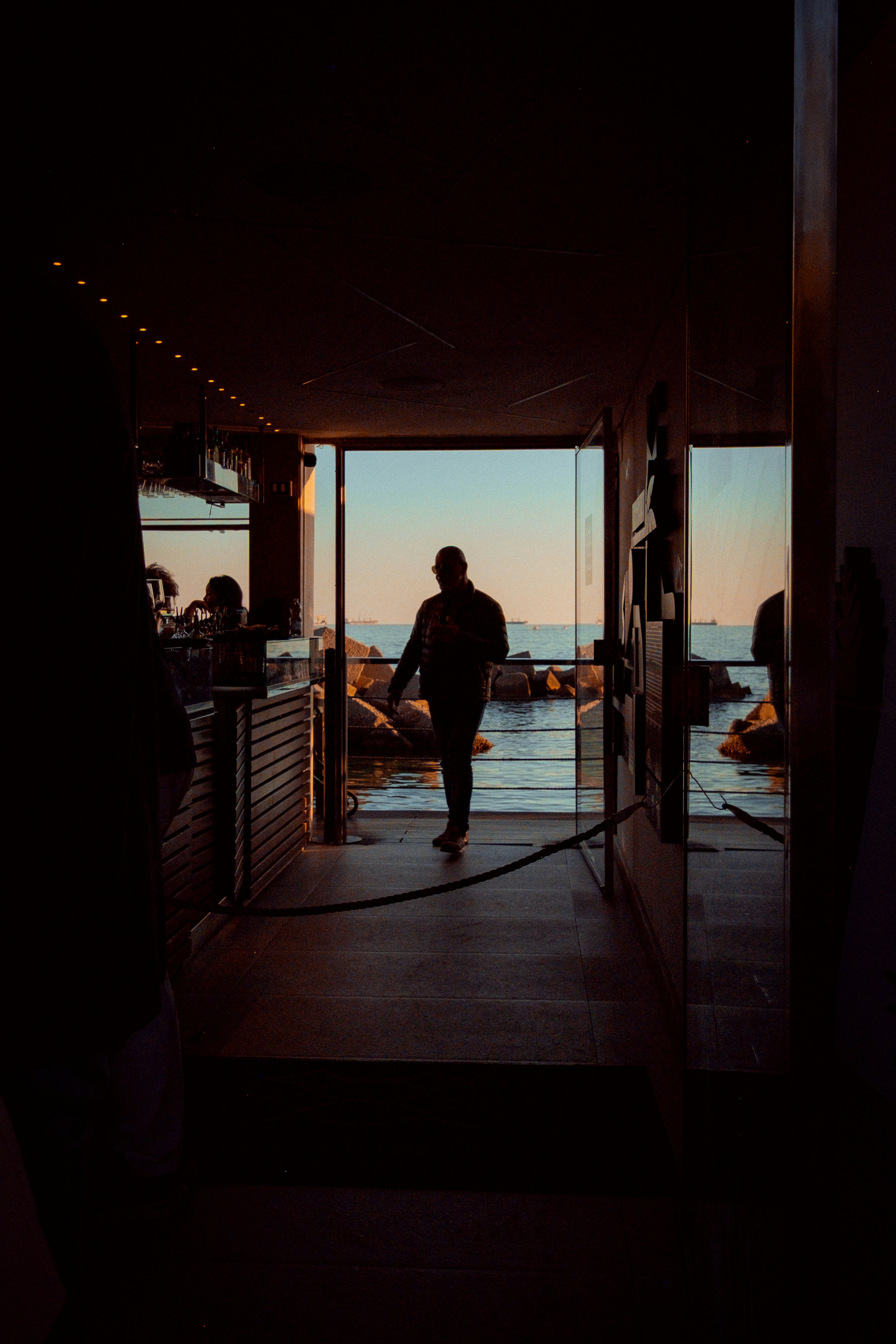 Emergence from Shadow: silhouette steps toward a sunlit harbor