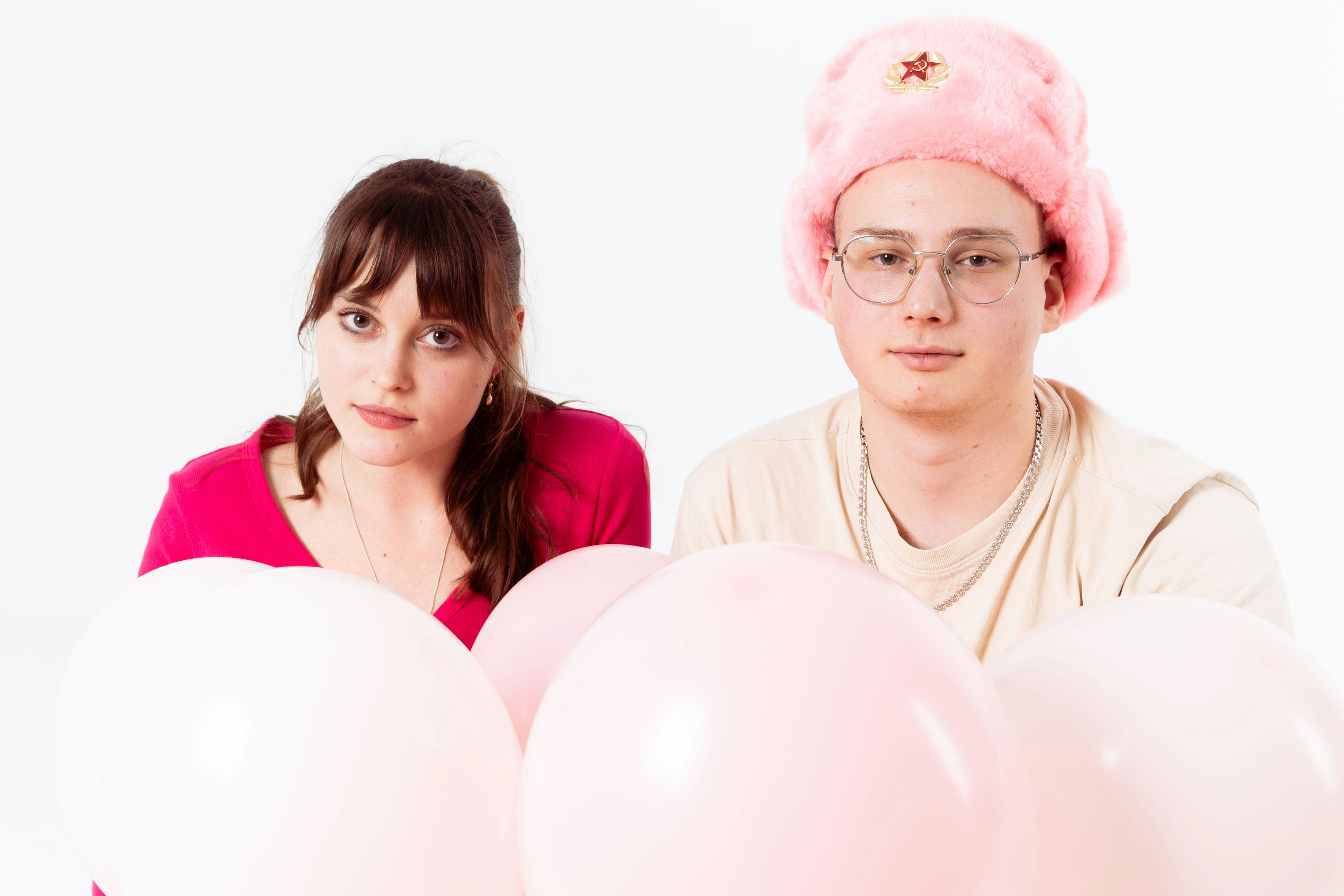 Two Friends Behind Soft Rosé Balloons in a Bright Studio