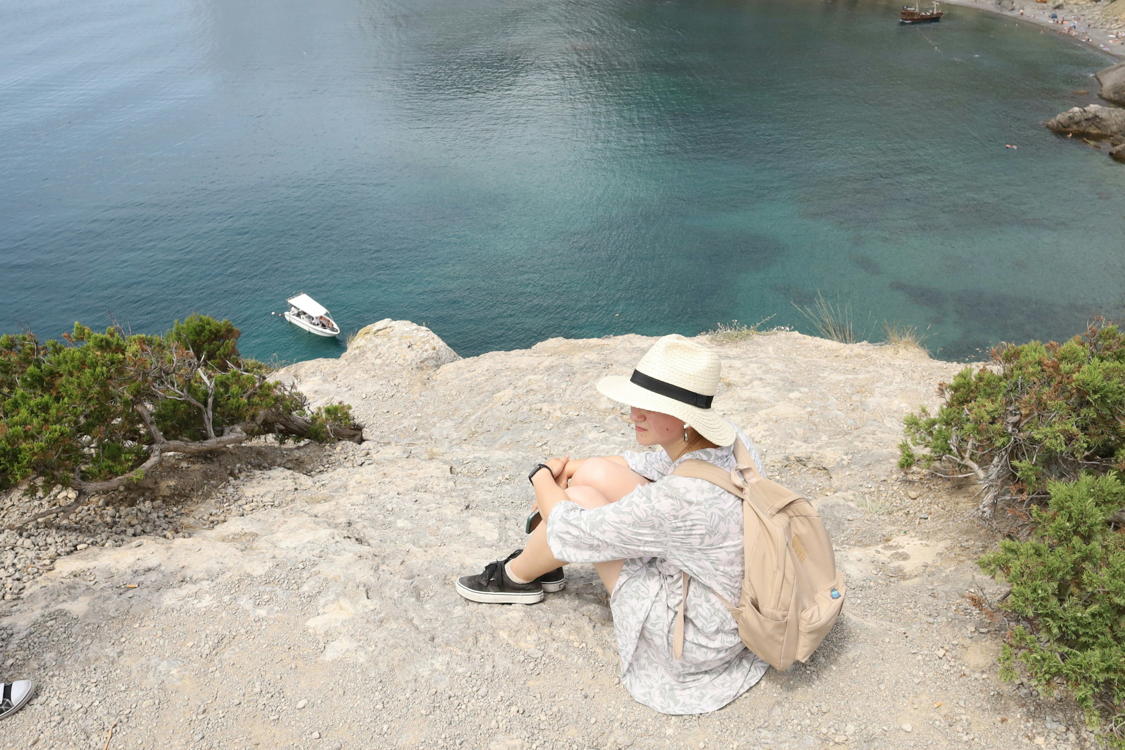 Seated traveler at coastal cliff edge watching the turquoise inlet