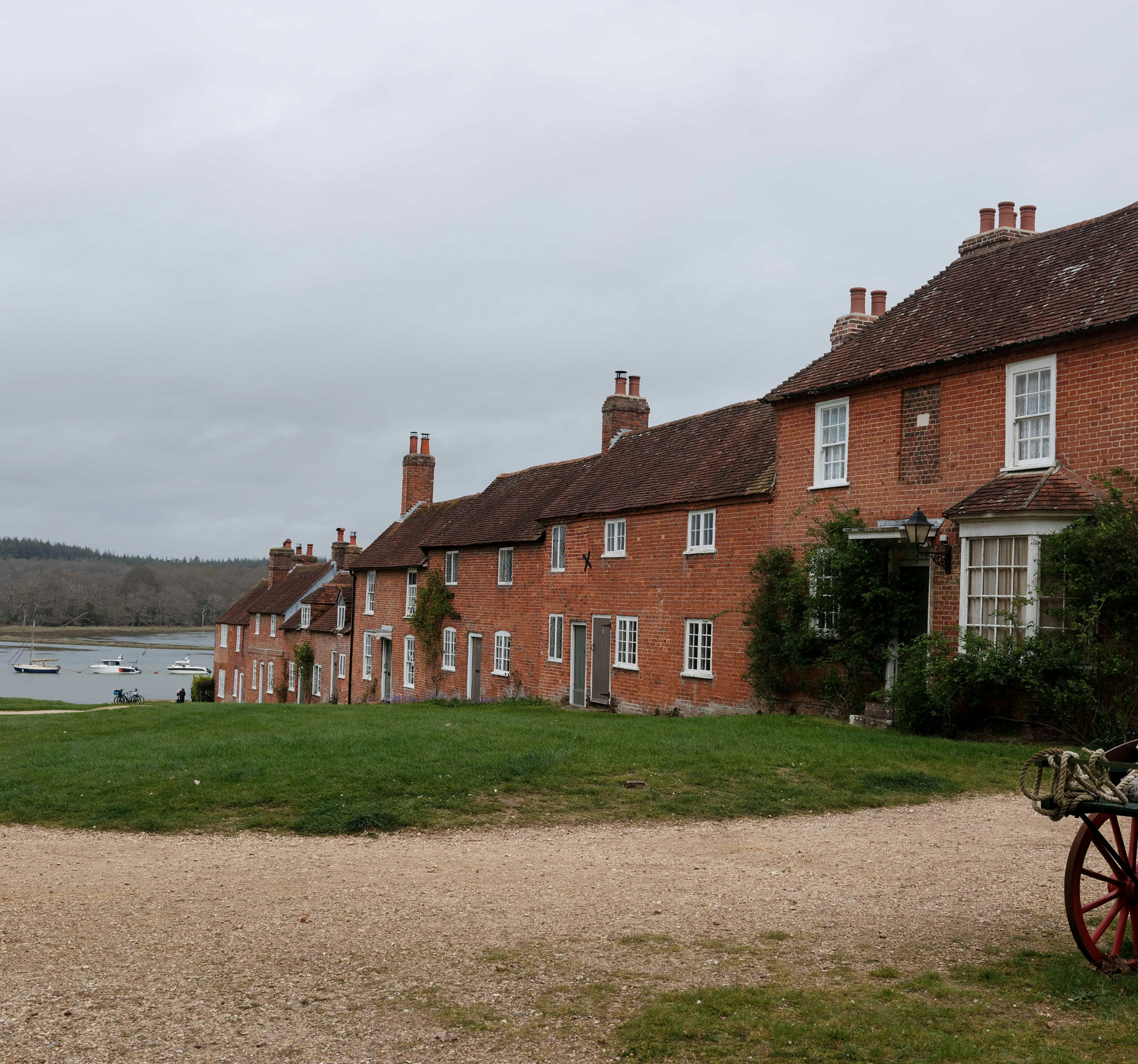 Row of brick cottages by the shoreline with a gravel foreground and a vintage wagon wheel