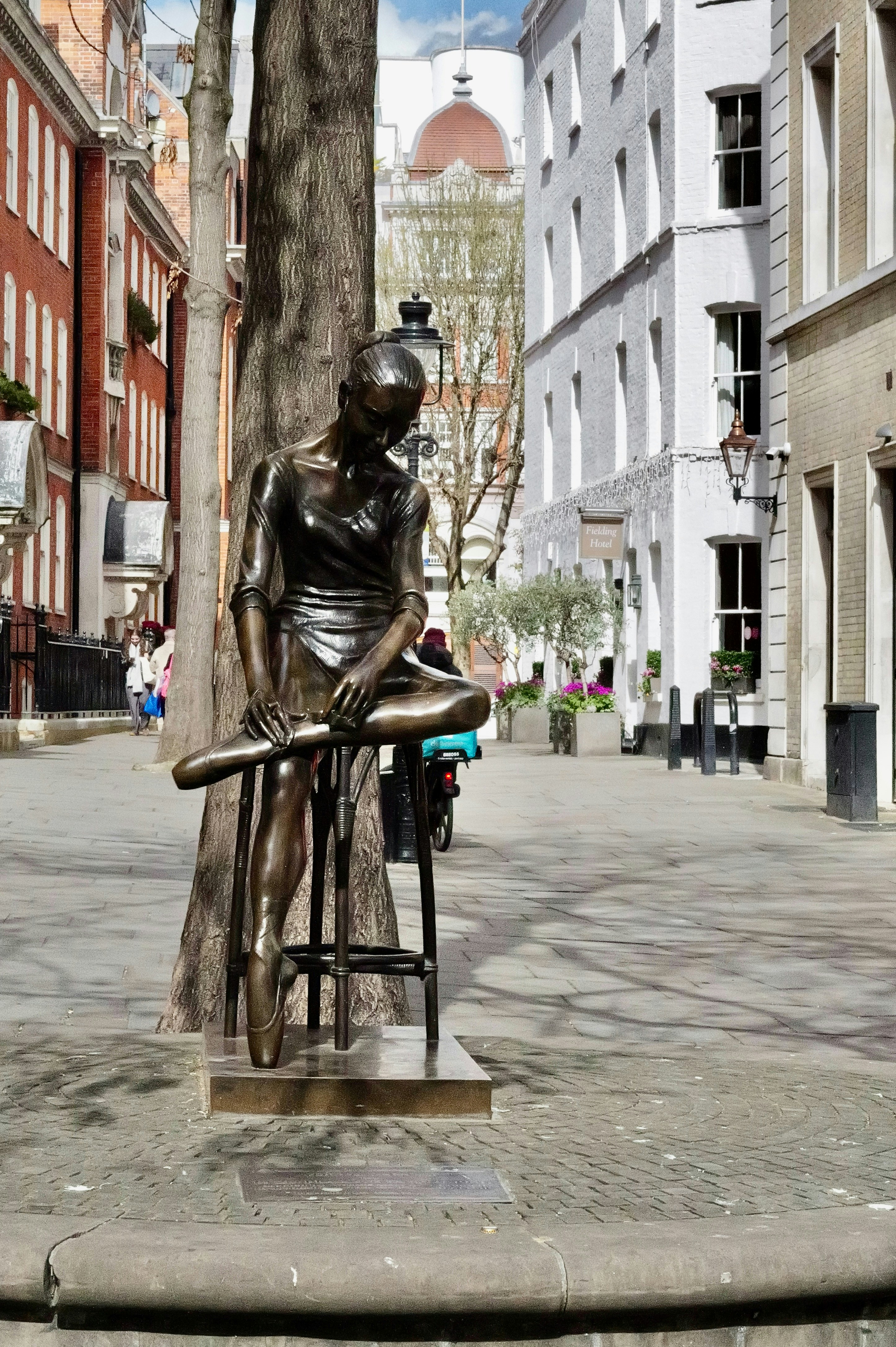 Statue in Motion: A Bronze Figure Paused on a Stool Amid City Facades