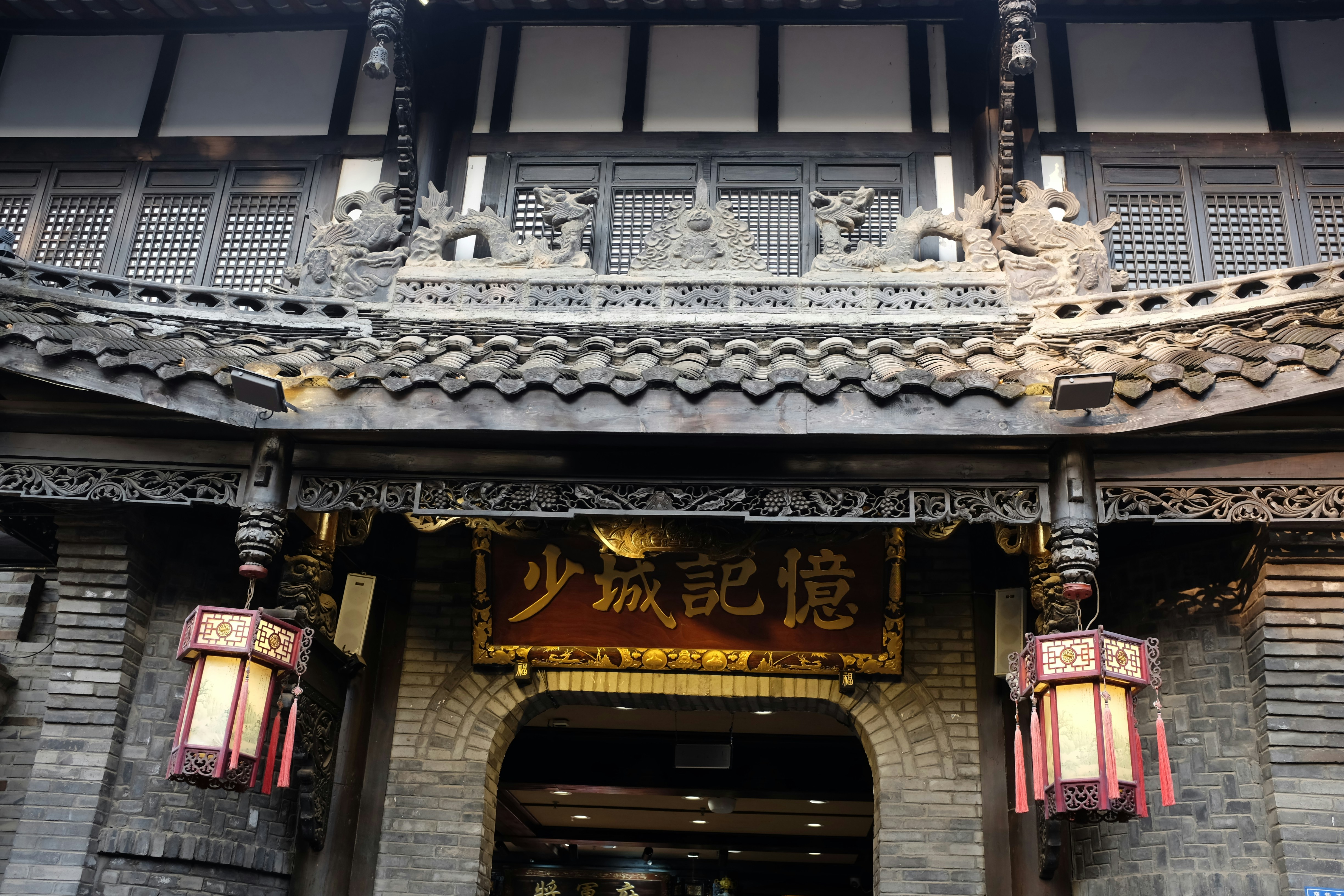 Ornate Temple Entrance: Carved Frieze and Lanterns Beneath a Gabled Roof