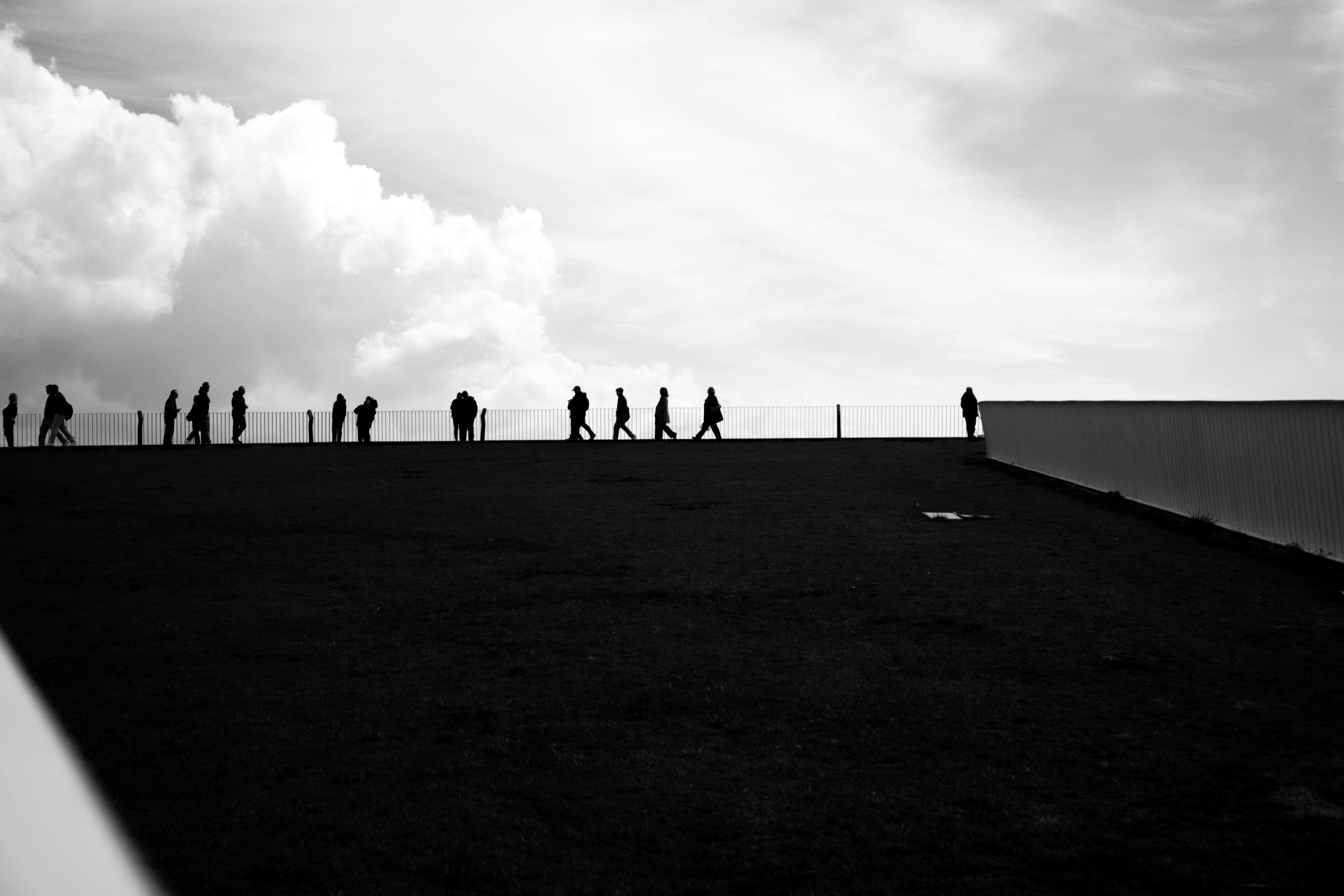 Line of silhouettes along a rooftop edge under a vast clouded sky