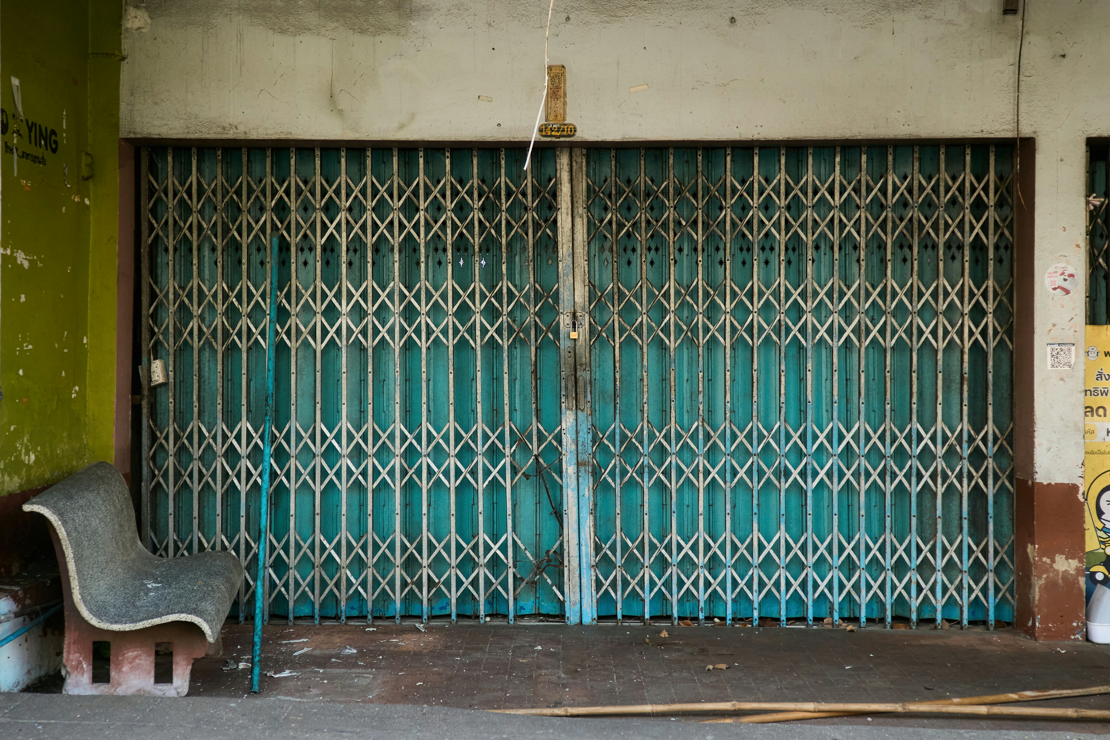Closed storefront with rusted lattice doors and weathered curbside seating