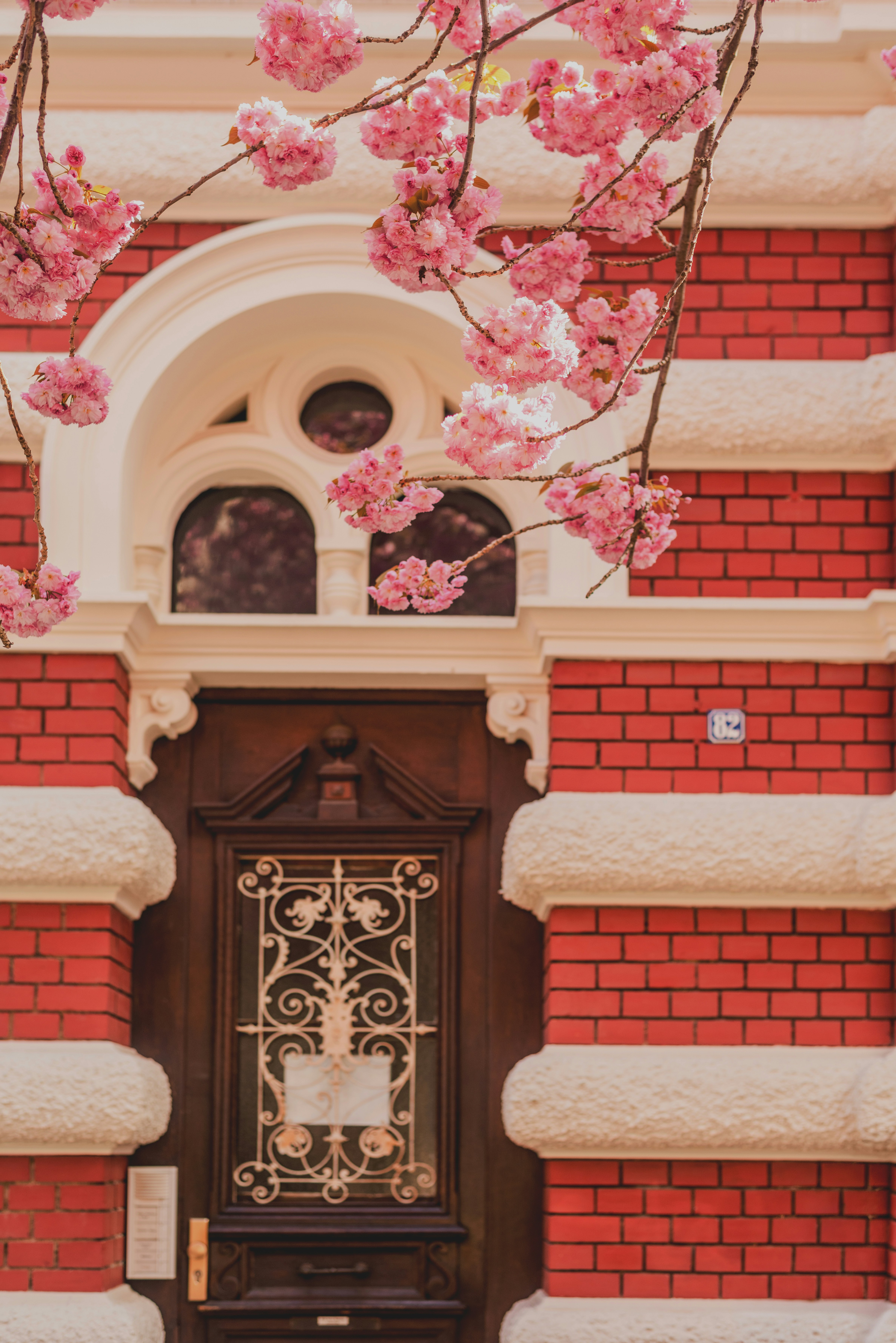 Blossoms Over Brickwork: A Wooden Door Framed by Pink Floral Arch