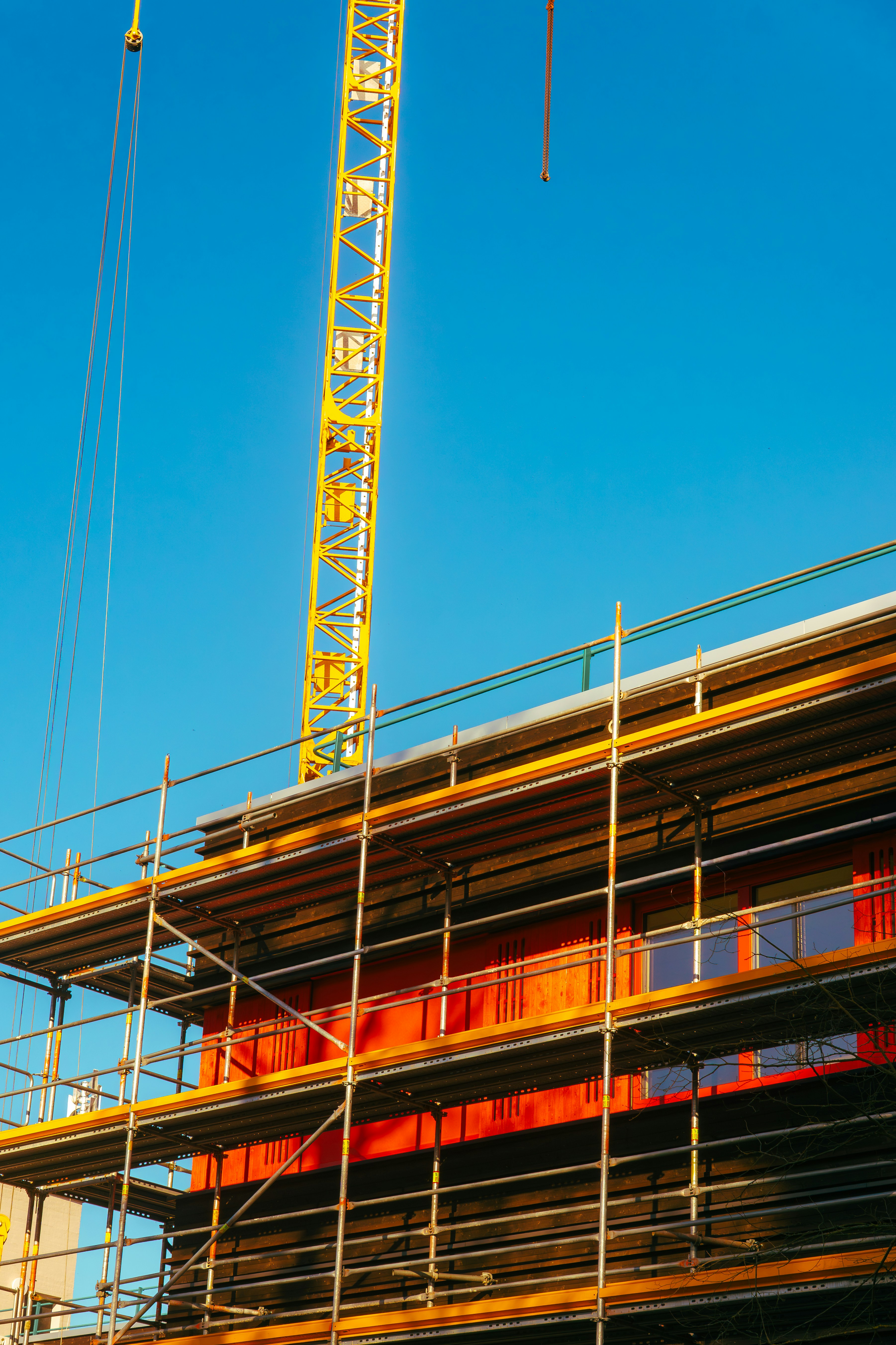 Tower Crane Above Red-Orange Facade: Scaffolding Lines in Sunlit Construction