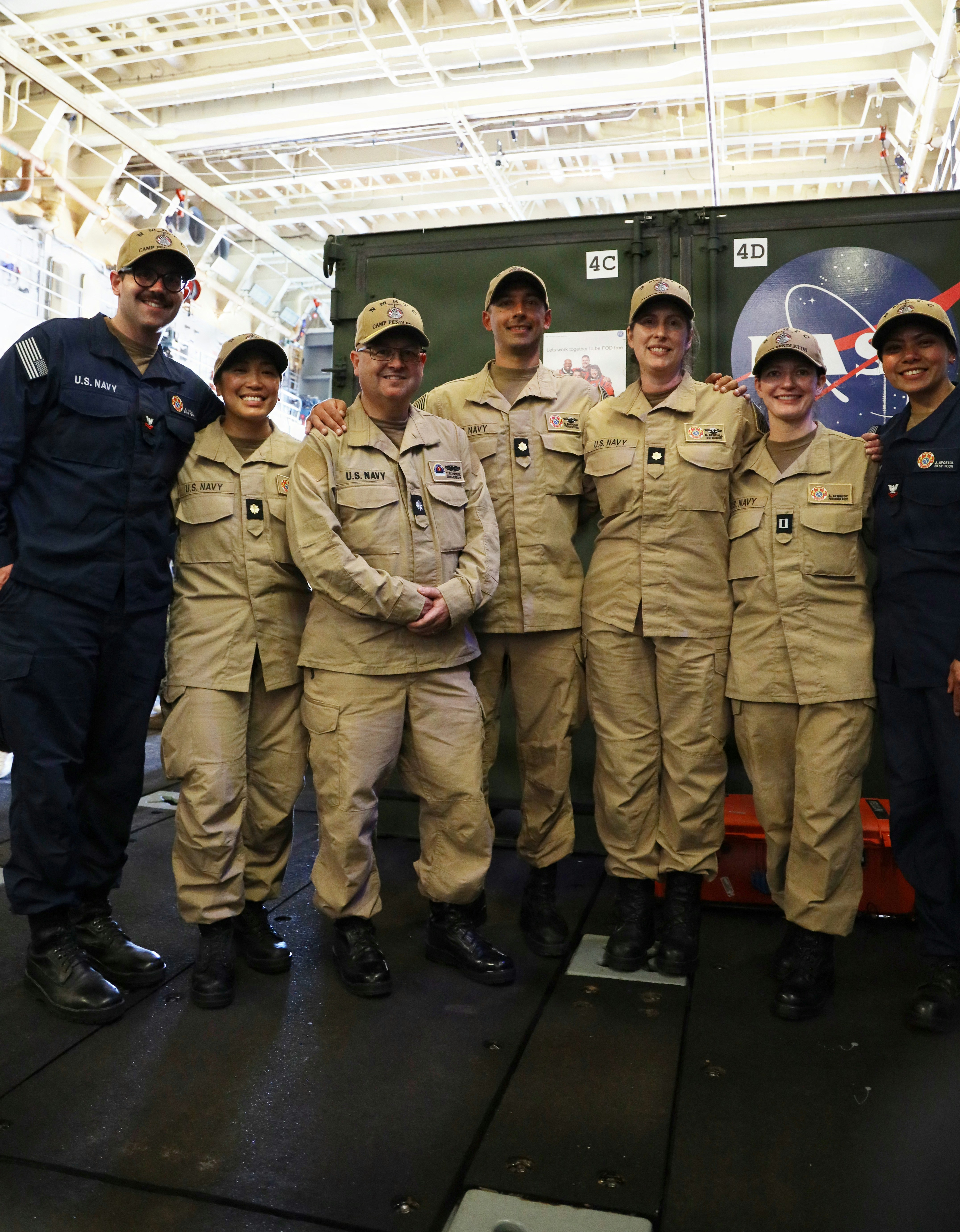 Crew of Navy Uniforms Stands in a Line Inside a Space Capsule Setting