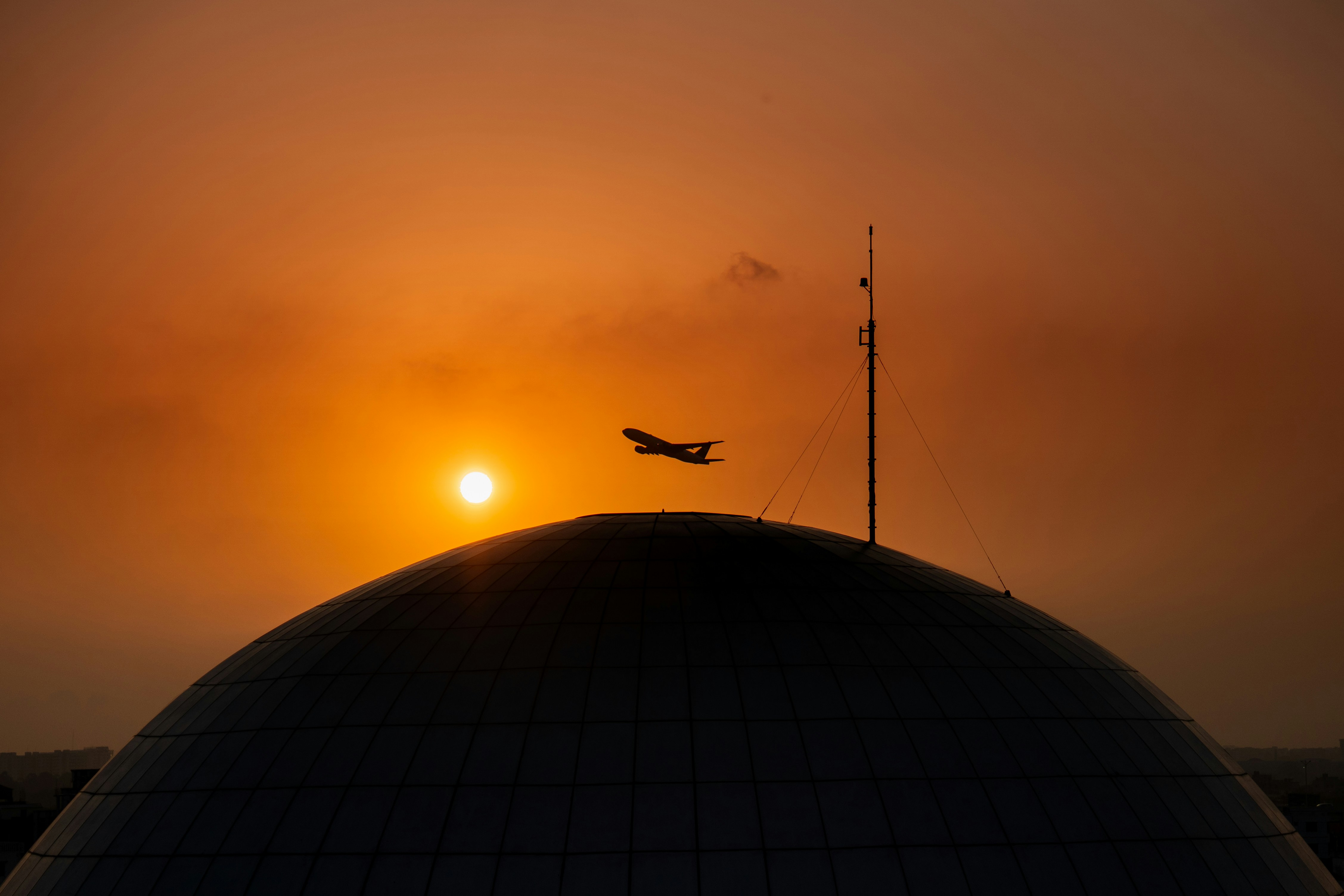 Sunset Soaring: A Jet Traces the Horizon Above a Dome