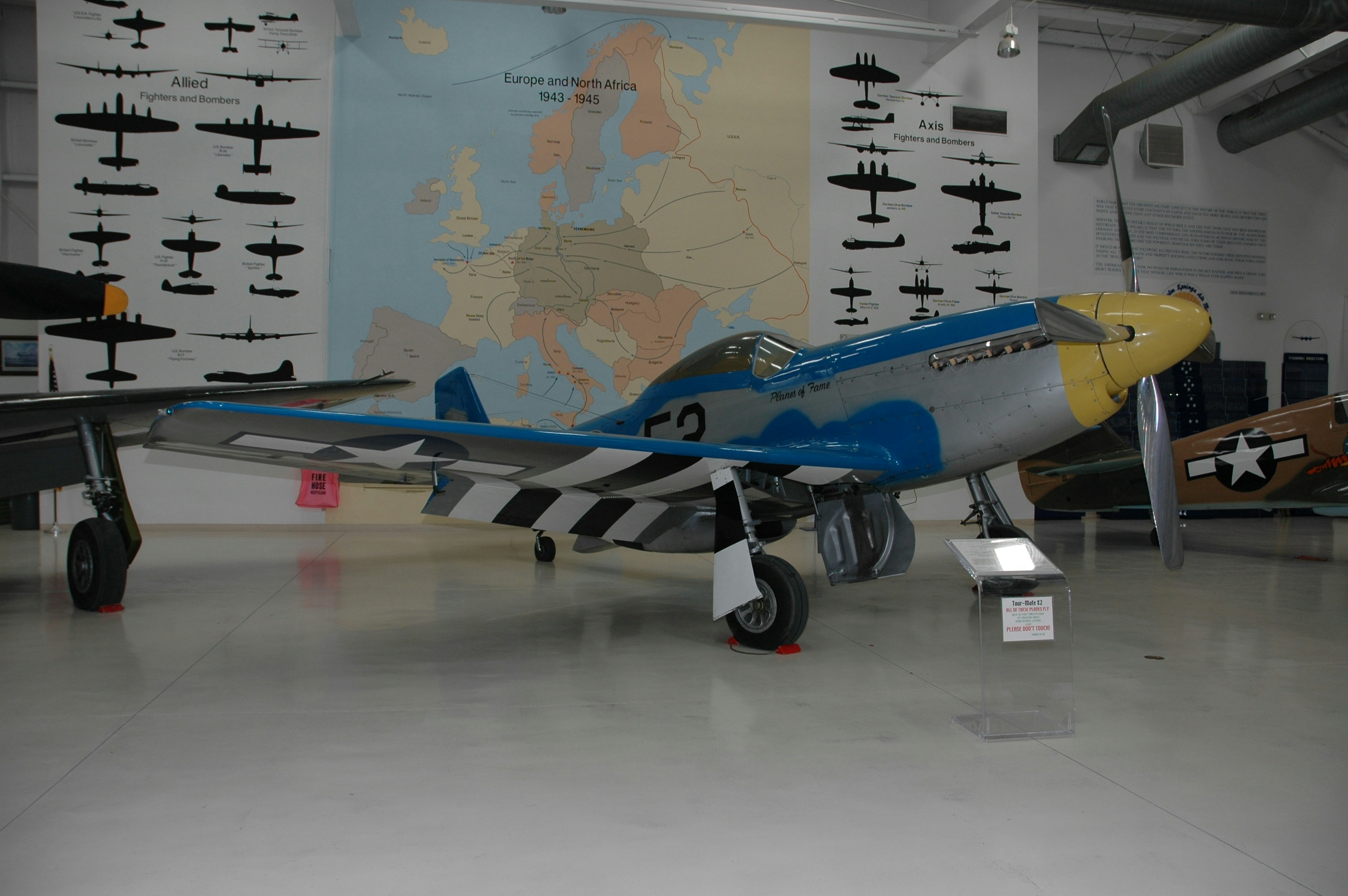 Blue and gold WWII trainer on display beneath a wall of silhouettes