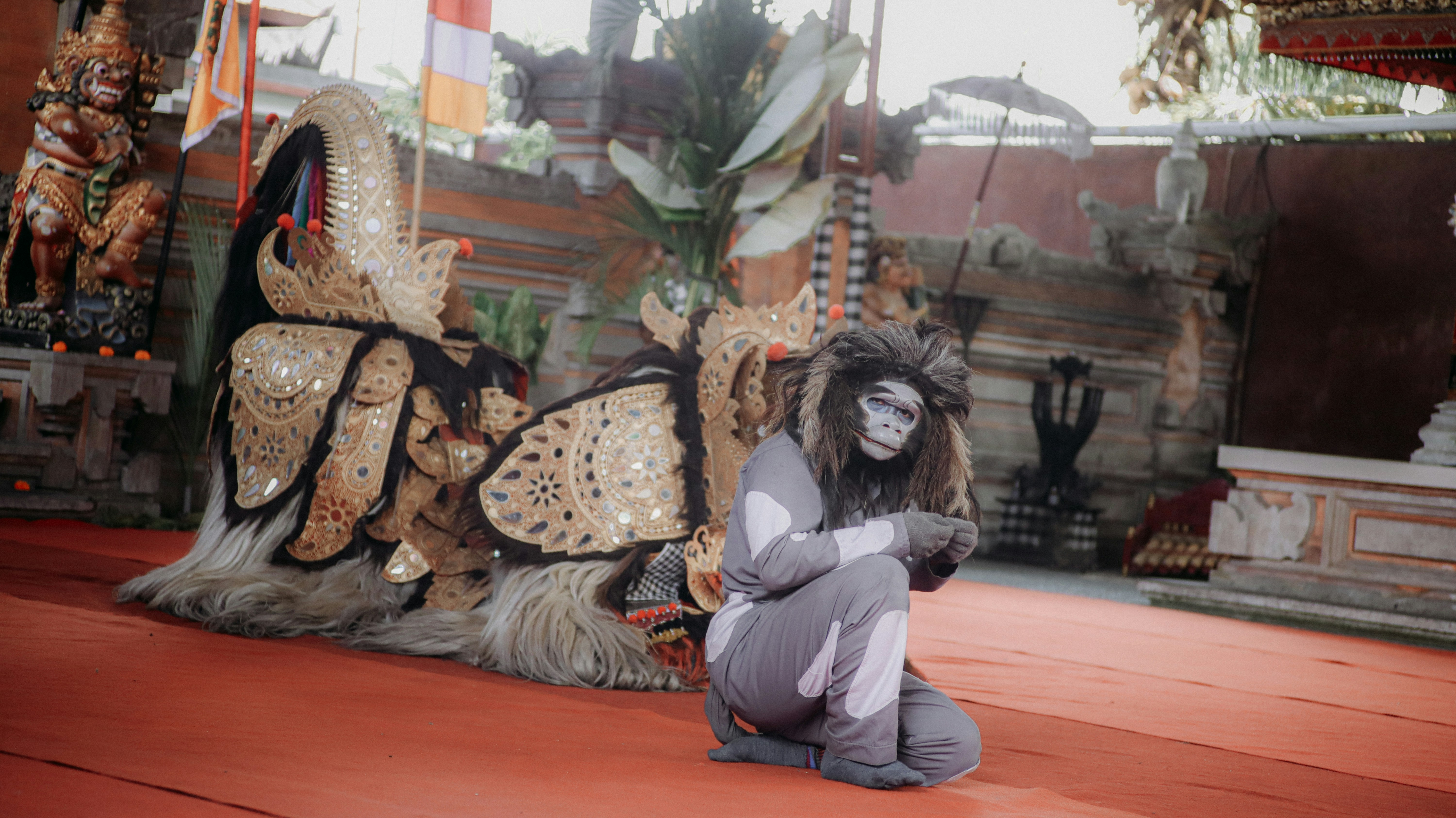 Masked dancer and ornate puppets on a red-carpeted temple floor