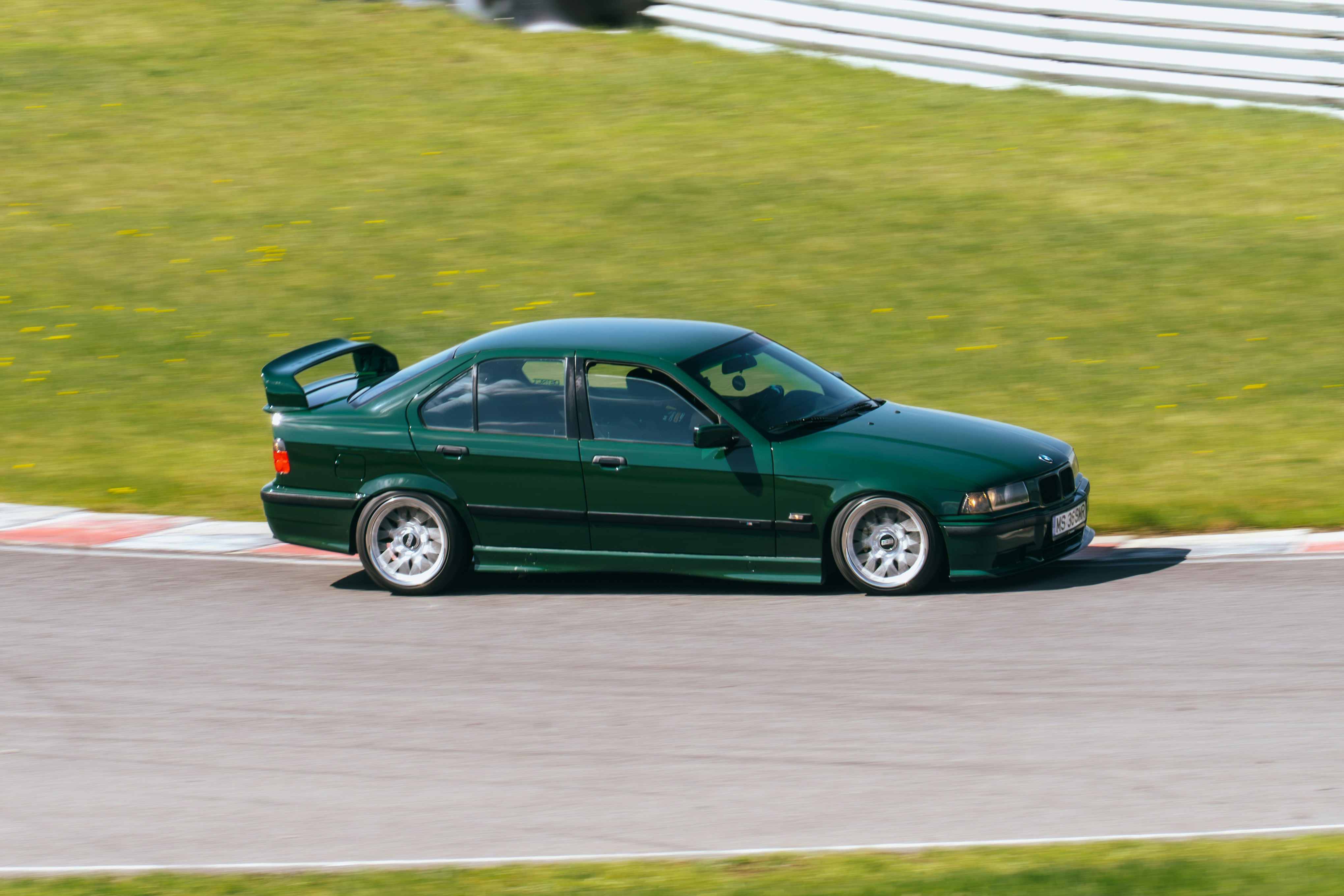 Green sedan in motion on race track with grassy backdrop