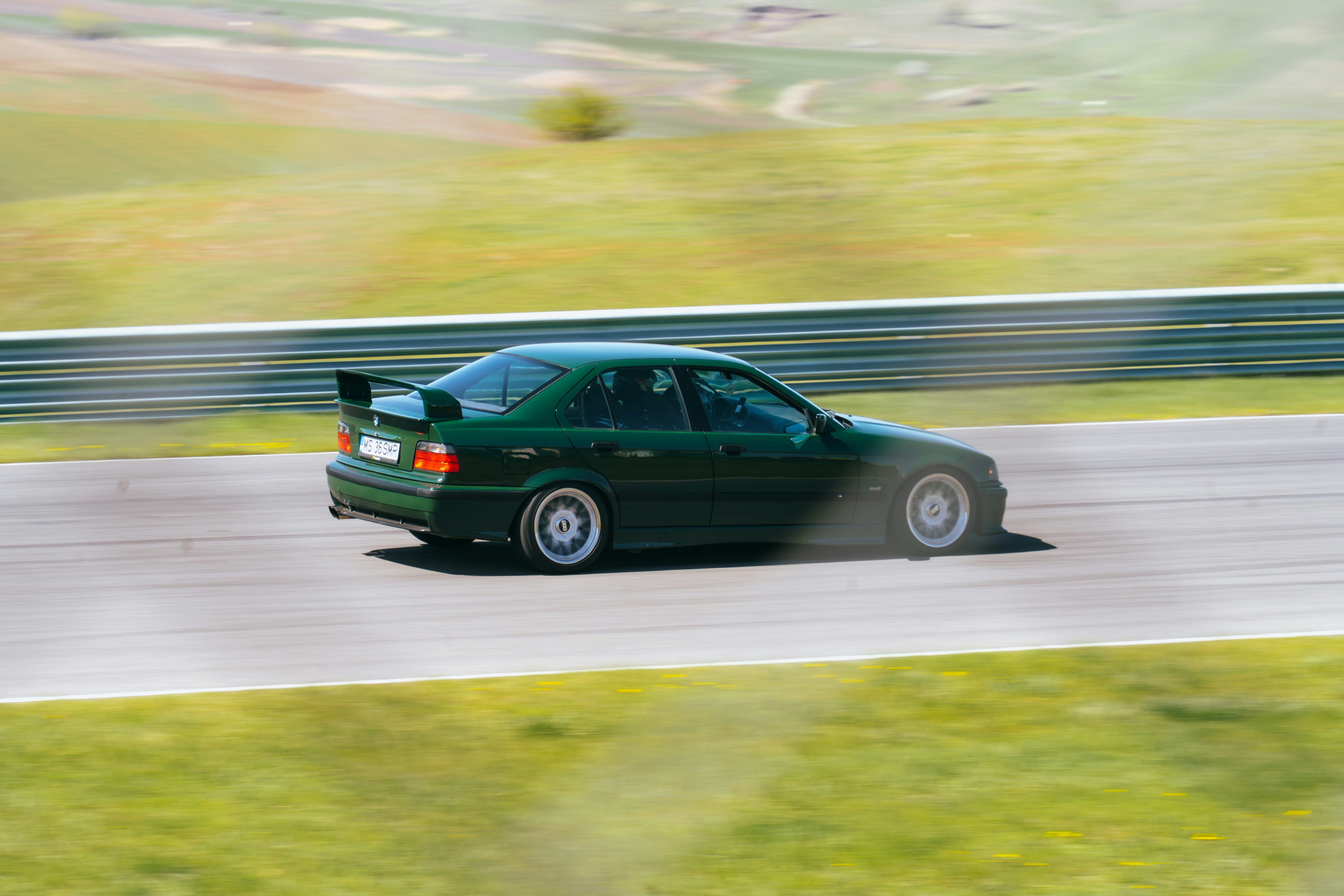 Green sedan in a wind-kissed blur on a sunlit track