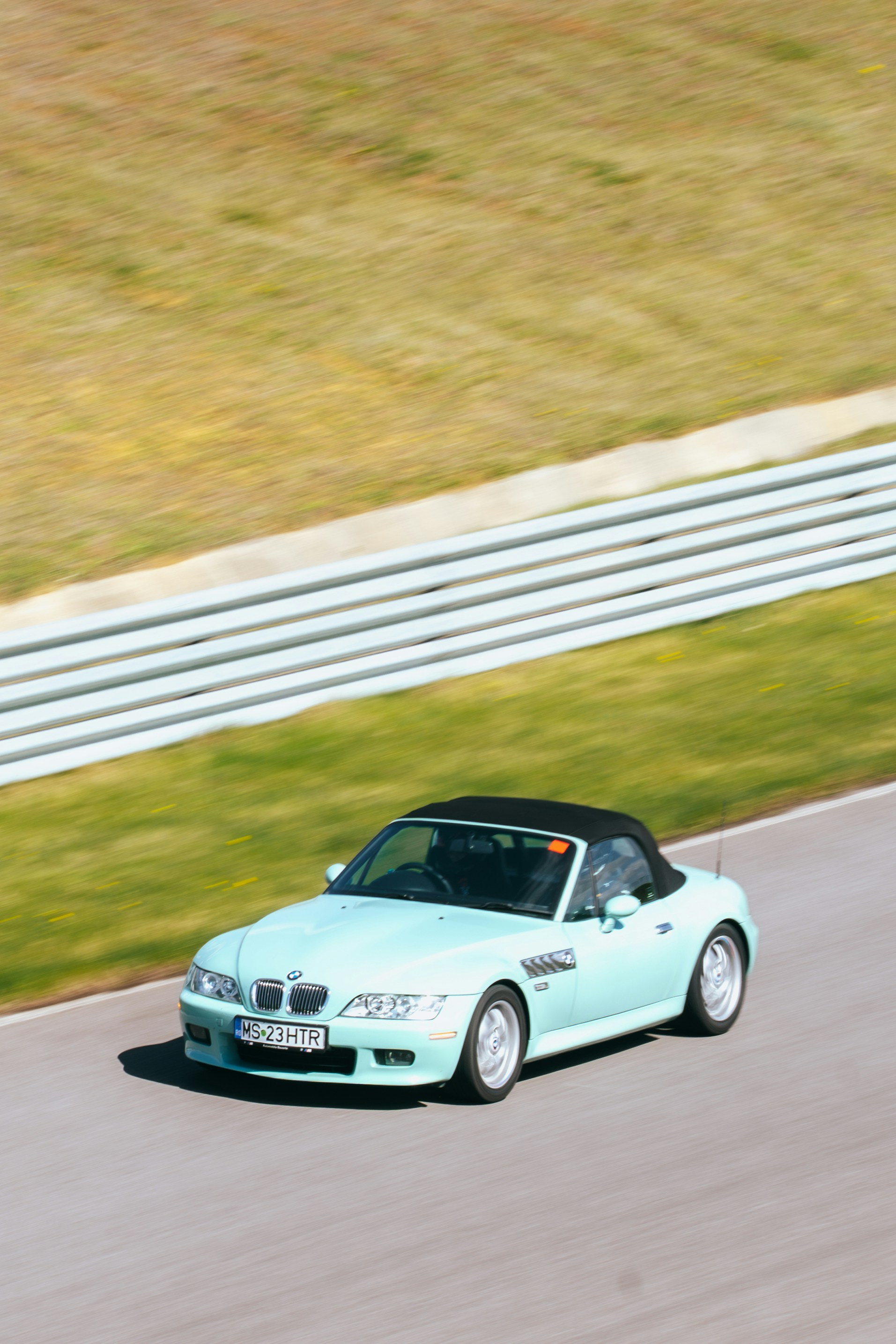 A mint-blue BMW Z3 Z4 roadster charges through a sunlit chicane