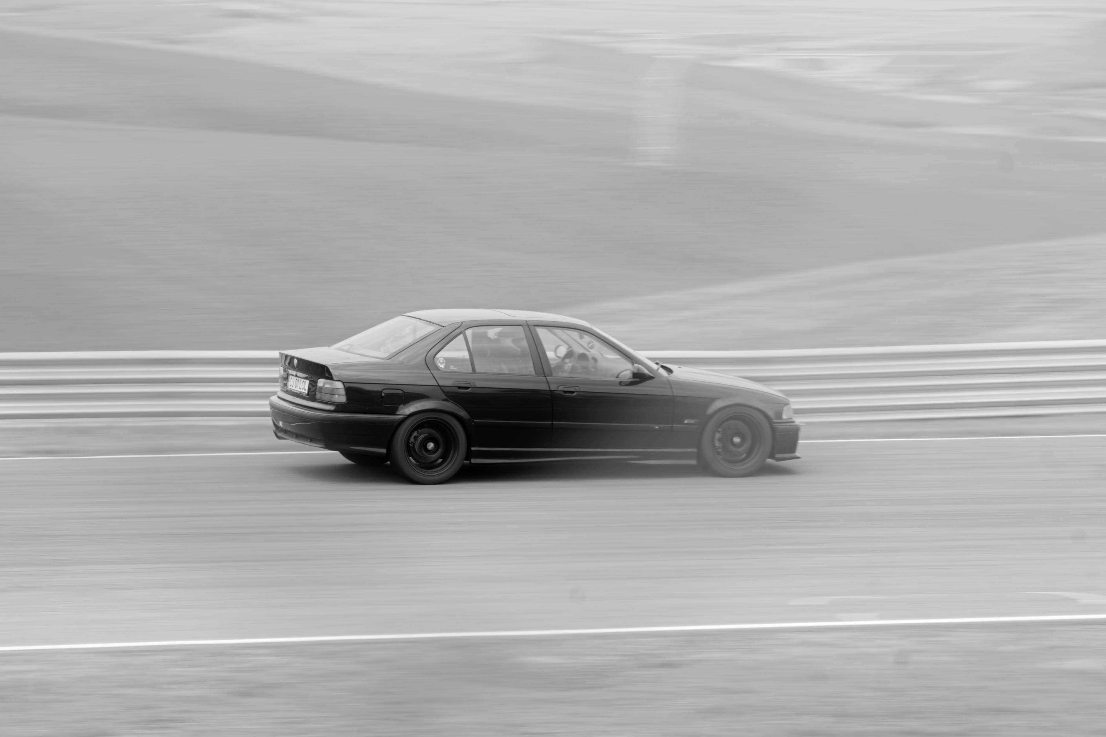Black coupe in motion on a race track with blurred guardrails and distant hills