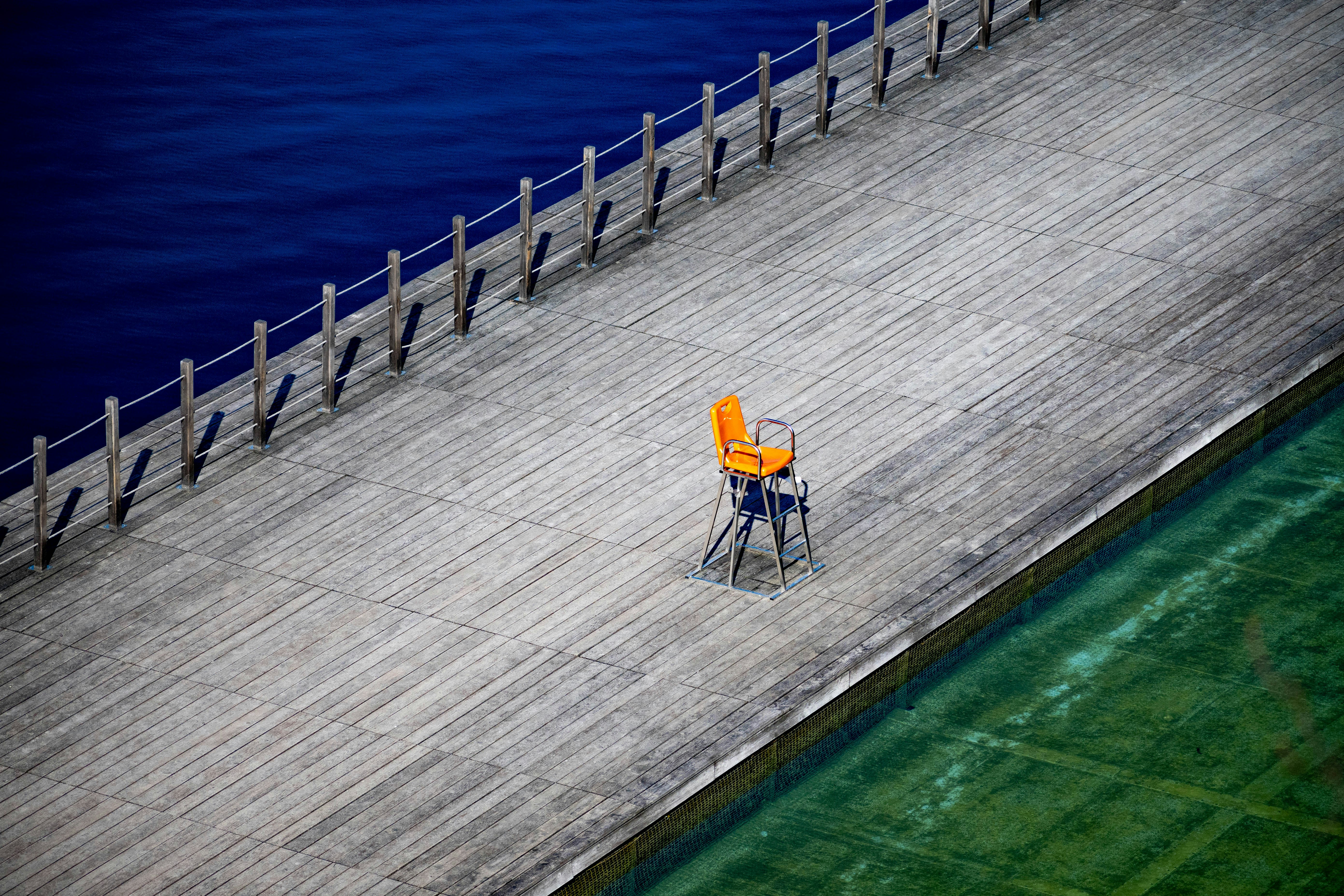Orange chair on a silent concrete pier by a turquoise tide