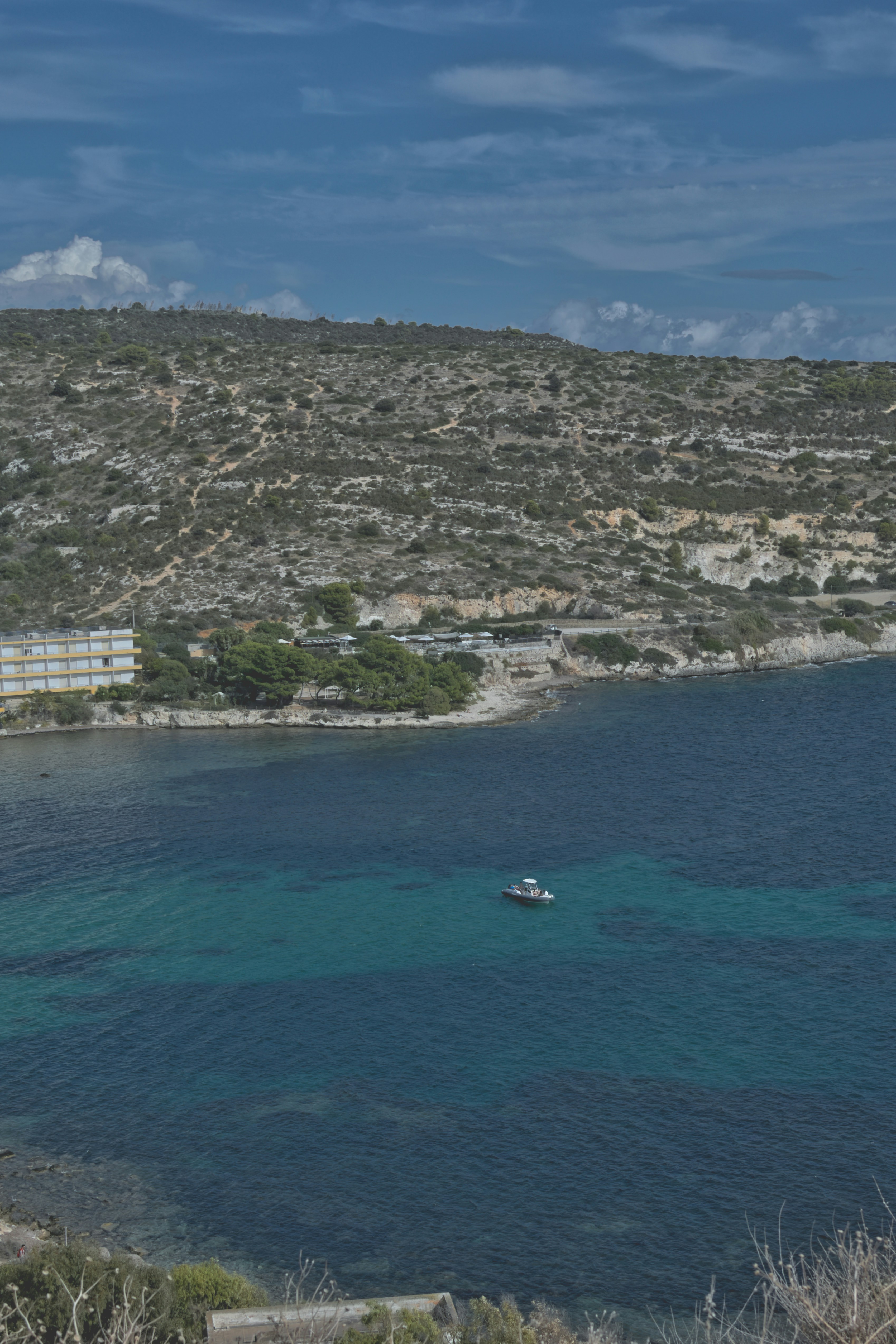 Coastal Outpost: A lone boat over turquoise waters framed by rugged hillside