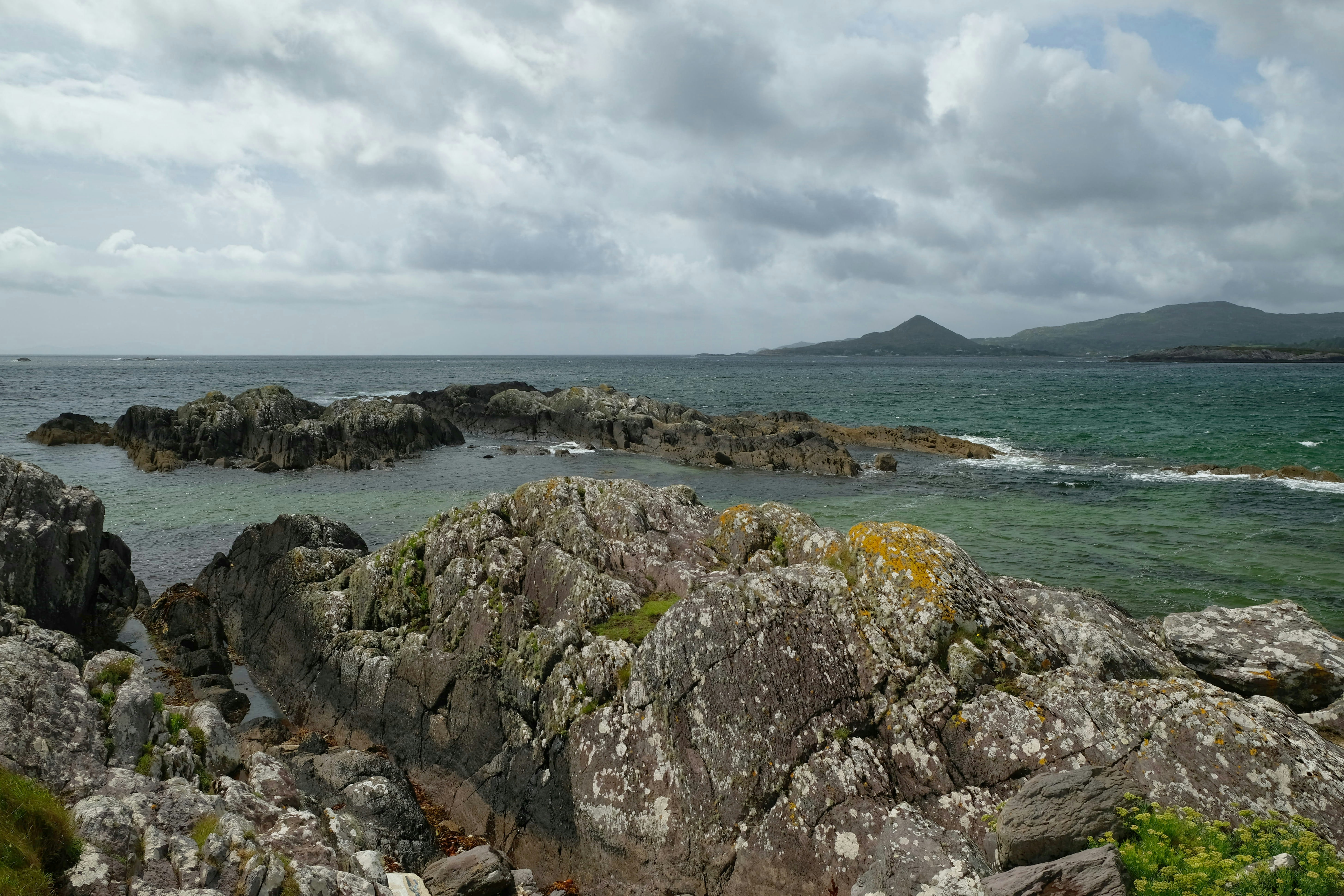 Rugged coastline under a moody sky, where lichen-streaked rocks meet the turquoise tide