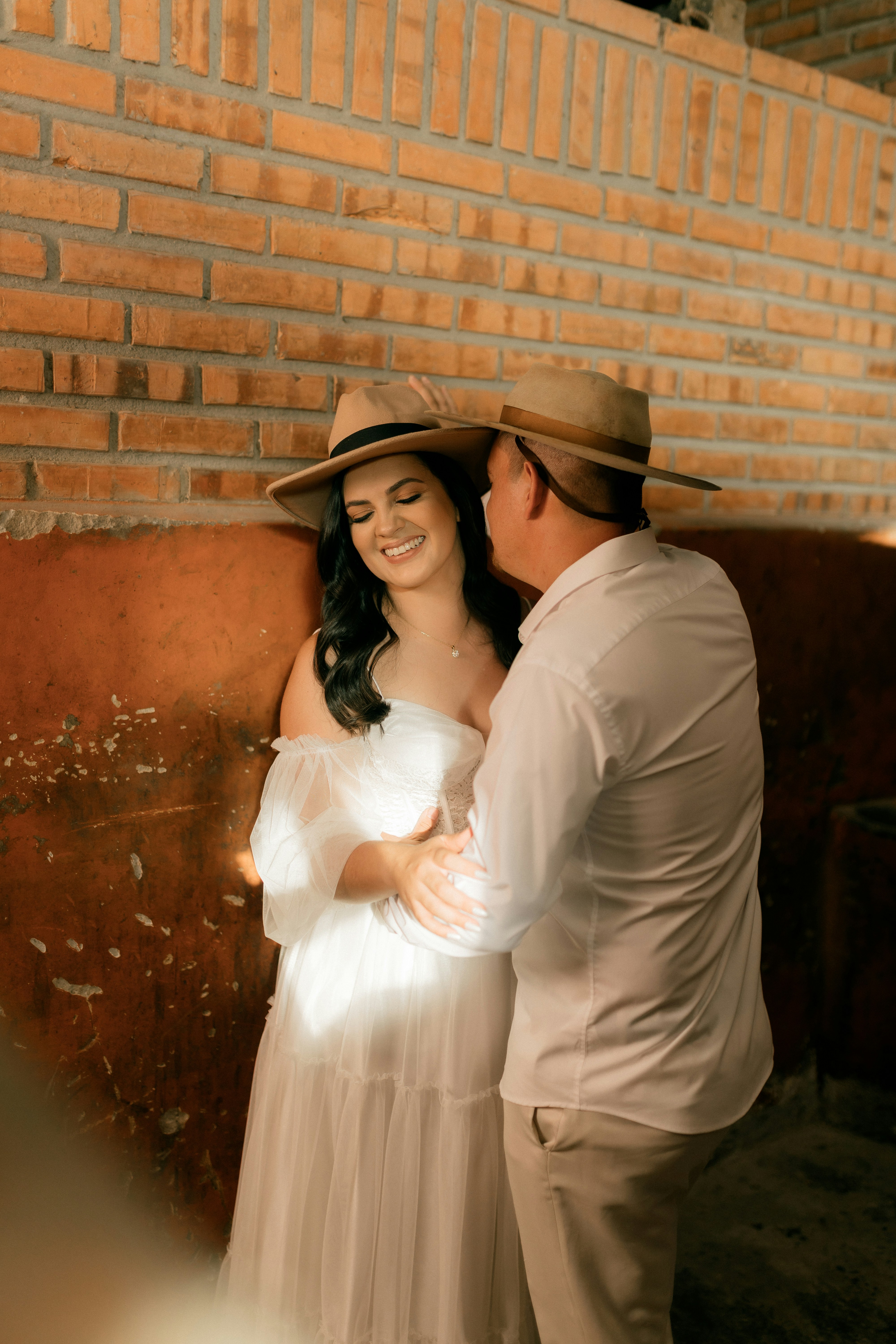 Couple in hats embracing near brick wall