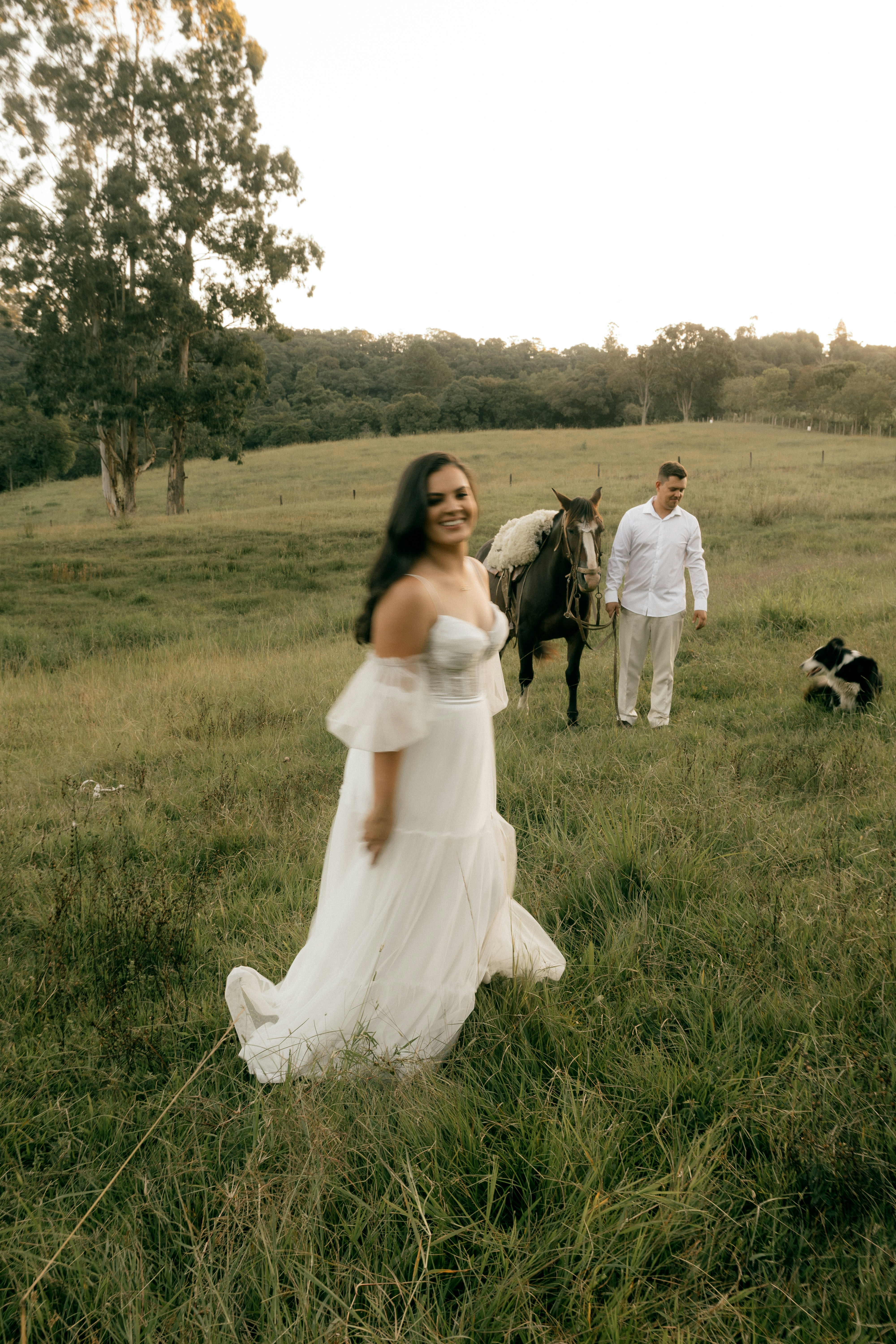 Bride in White Amid Fields, With Groom and Horse in Soft Evening Light