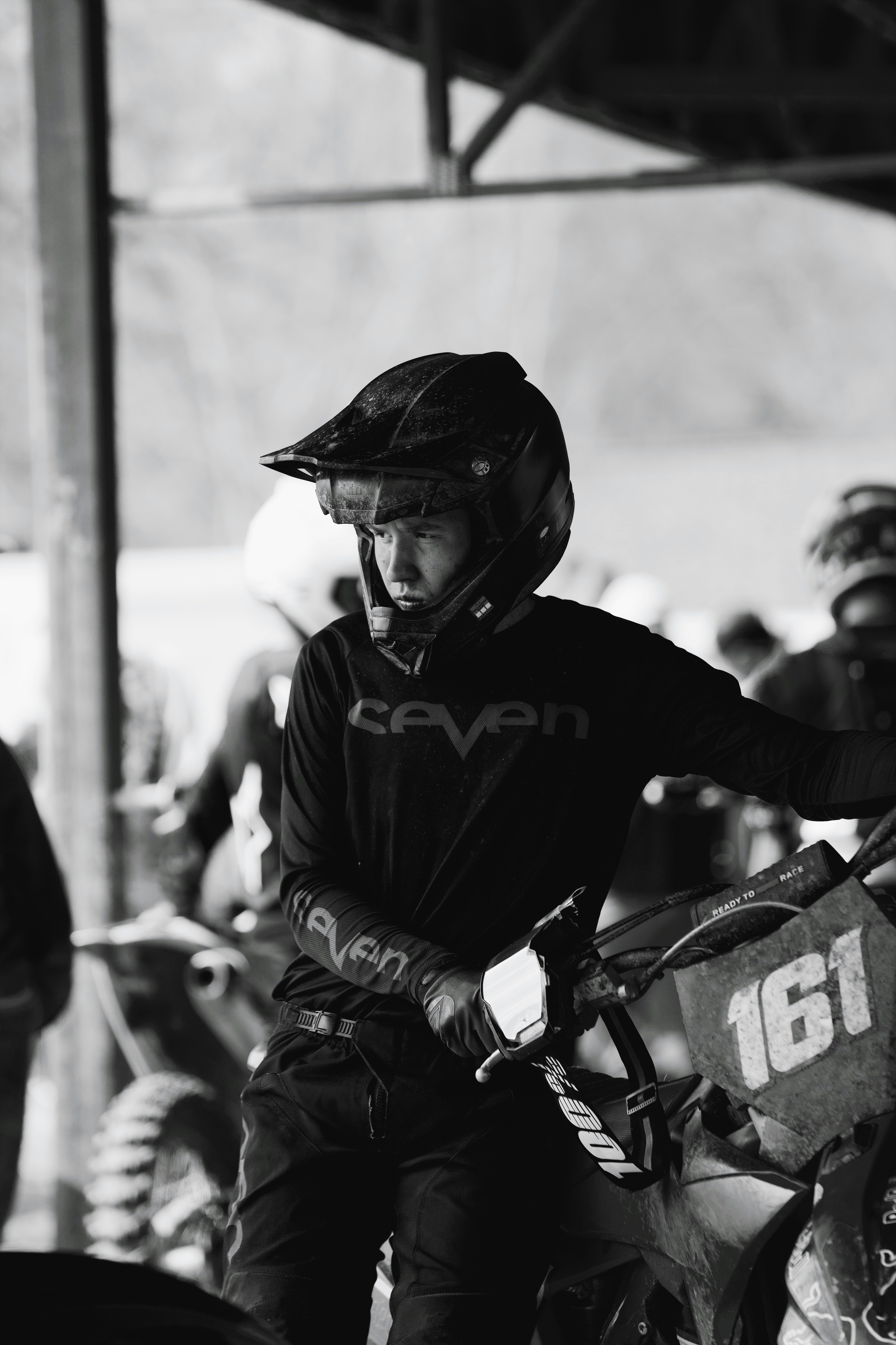 Chrome and Focus: Rider in a Black-tleeed Helm under the Racing Shelter