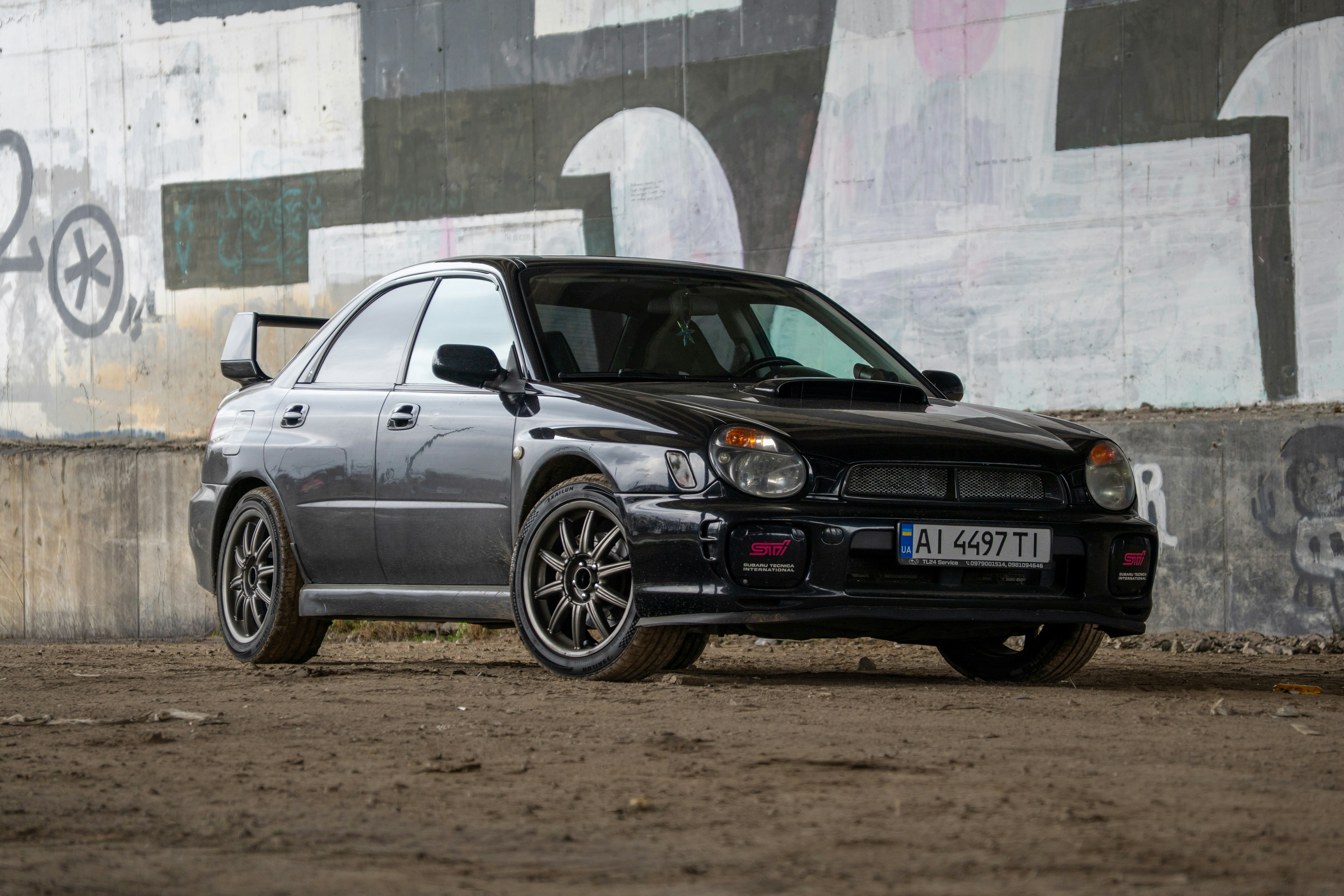 Dark-blue sedan on gritty lot under graffitied wall