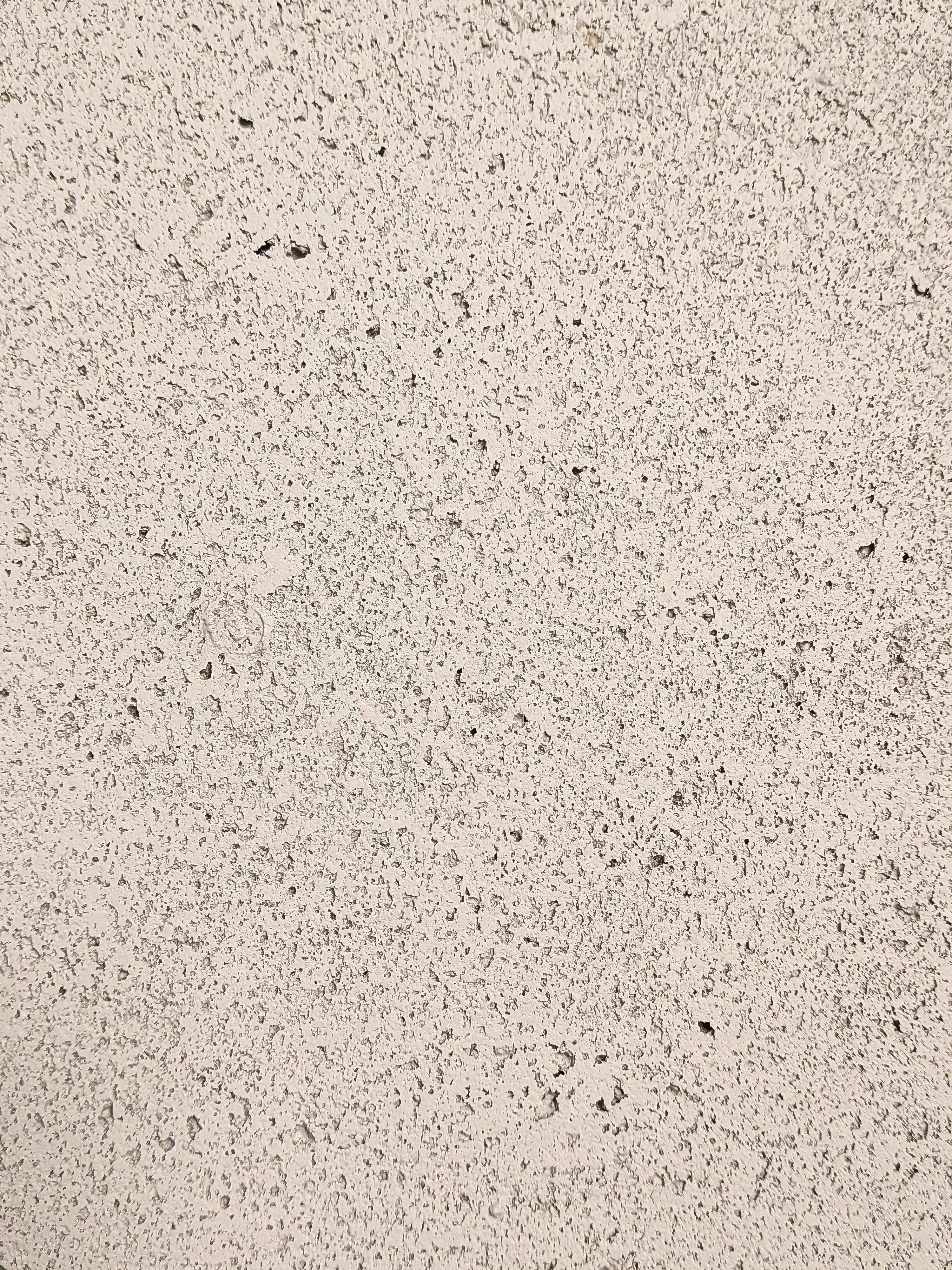 Close-up of sandy, grainy surface with small dark specks and irregular pores; a minimal, abstract texture suitable for background use.