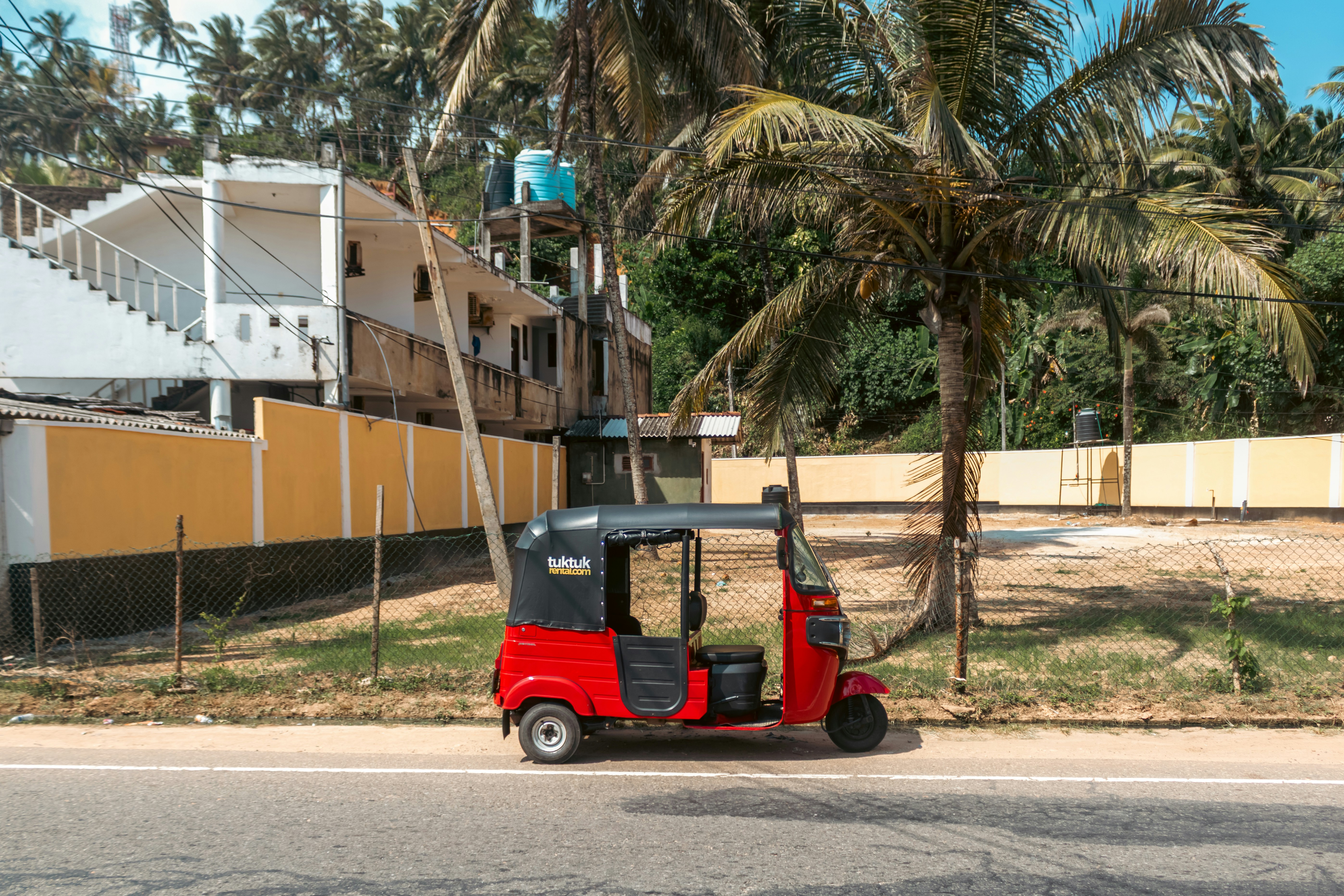Red Tuk-Tuk by a Sunny Fence