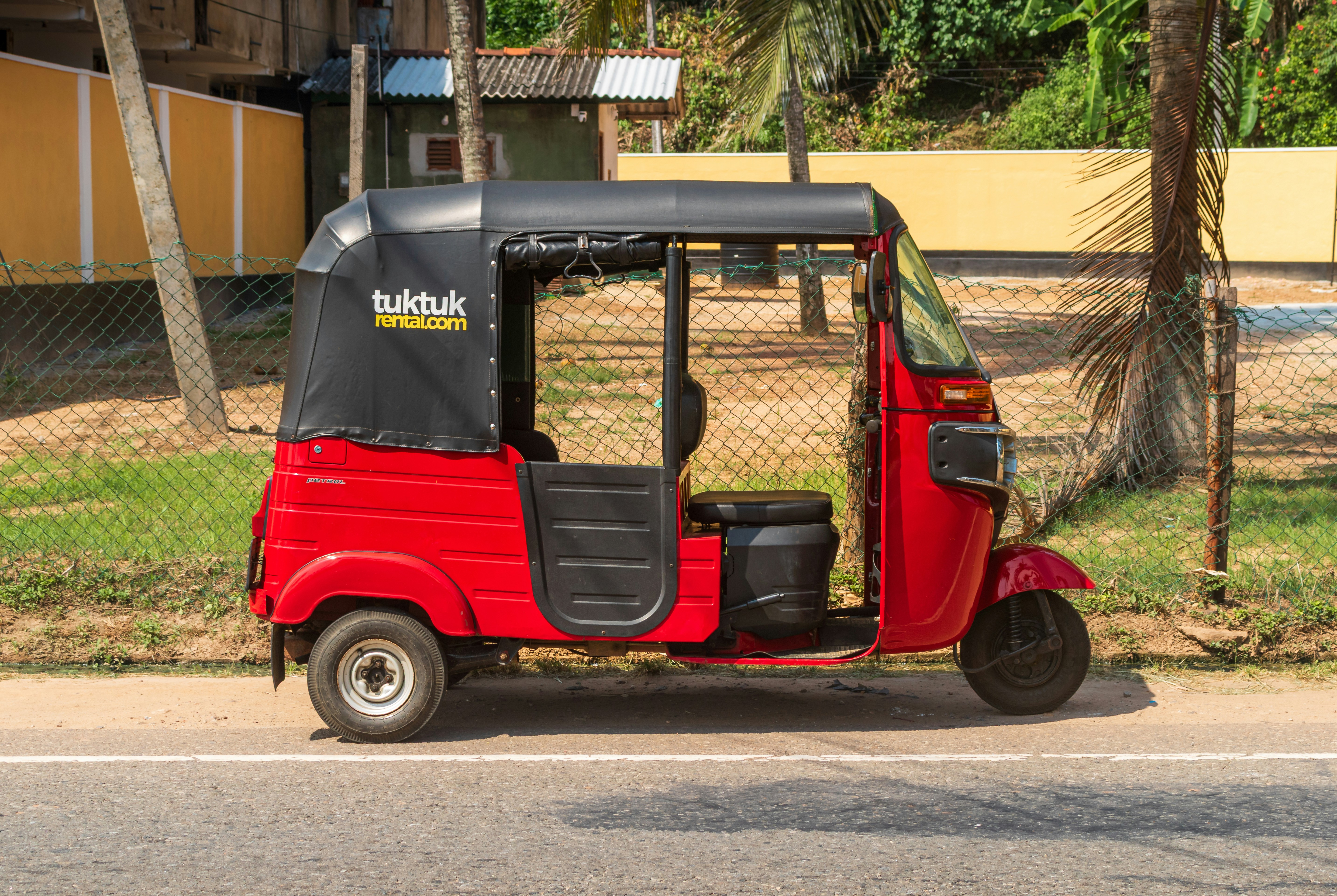 Bright Red Tuk-Tuk parked along a sunlit street behind a yellow wall