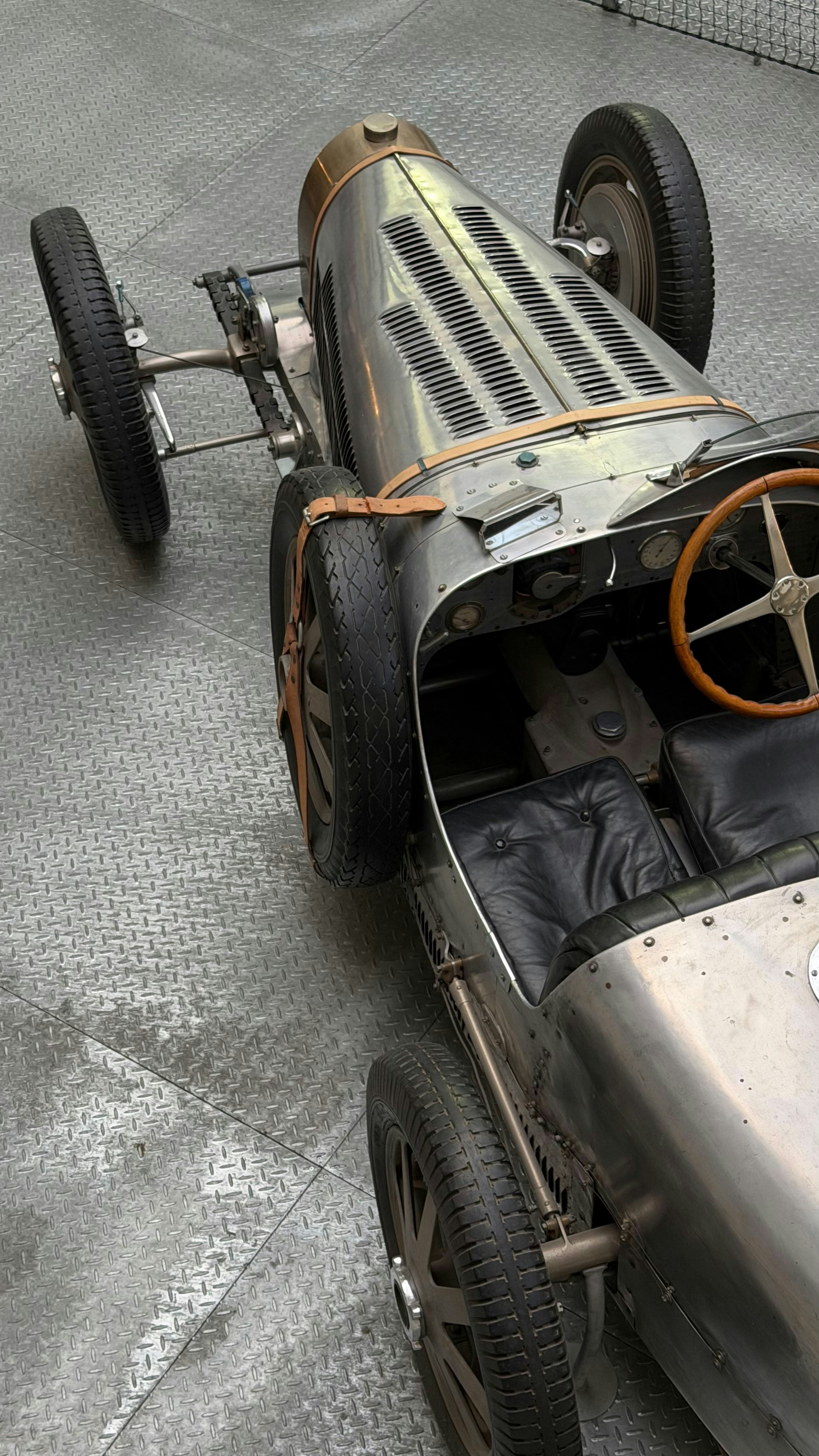 Brushed metal vintage racer: cockpit and steering wheel beneath perforated hood