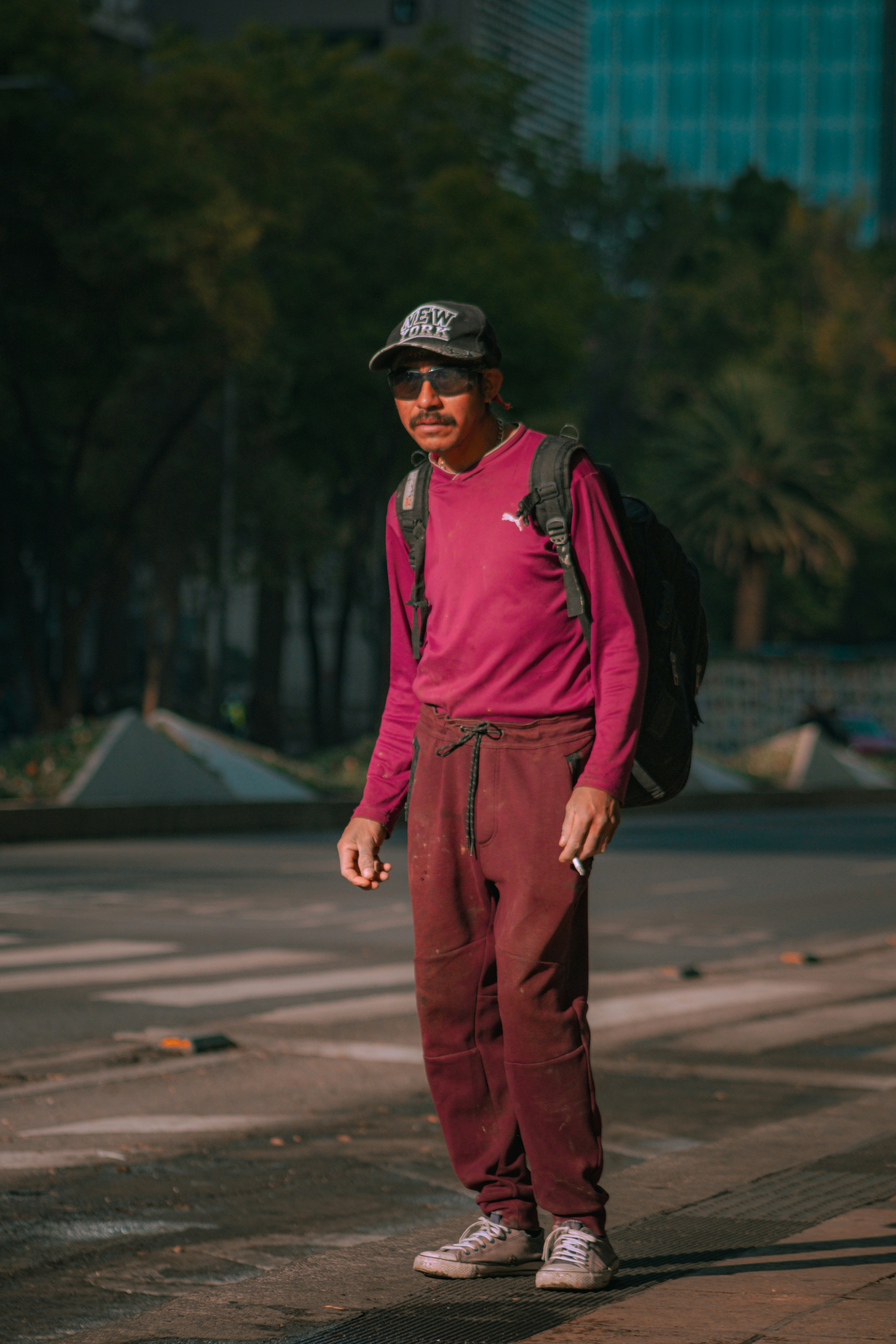 Man in Magenta Hoodie Standing with Backpack under Urban trees