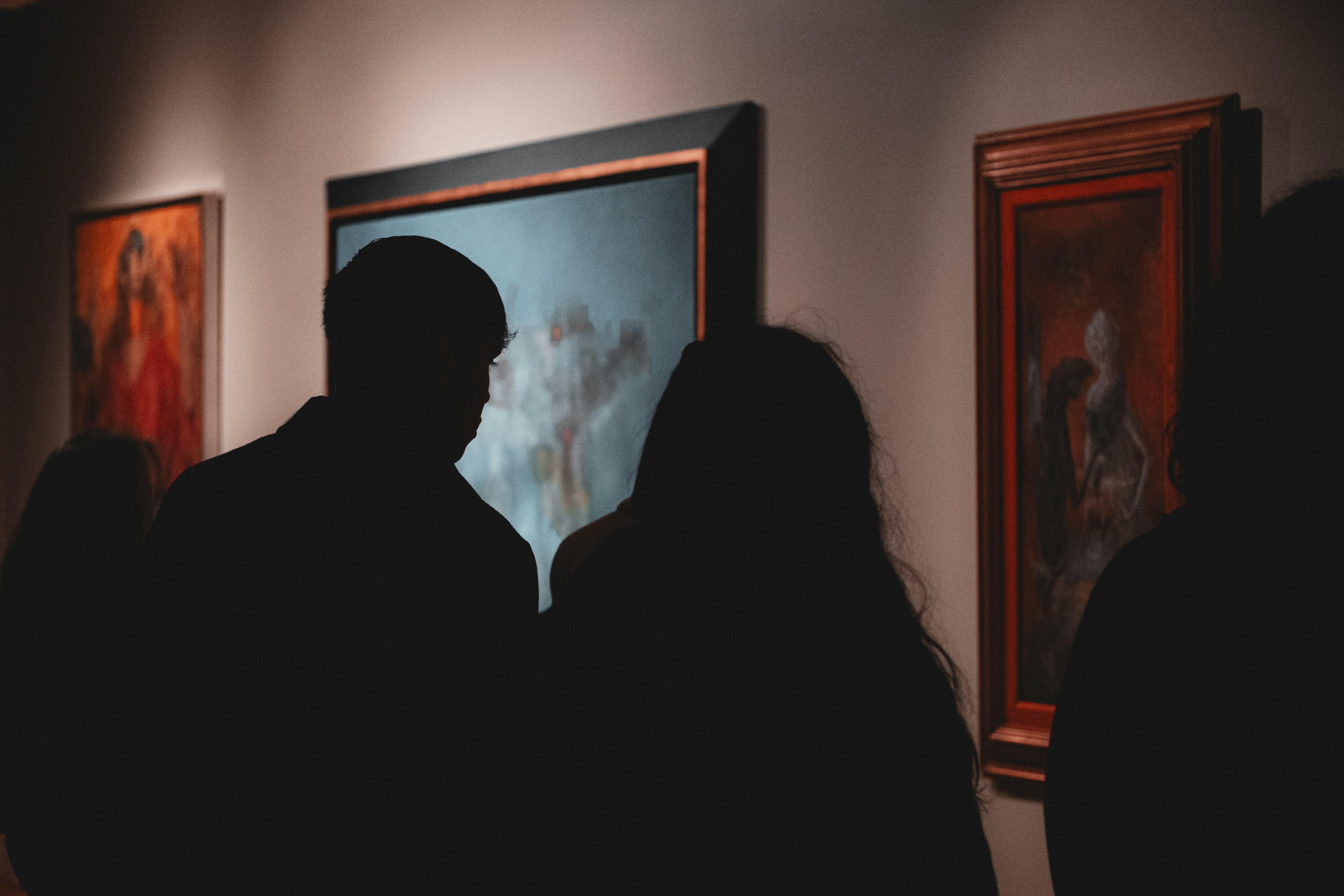 Silhouetted Visitors Contemplate Frames in Low Light Gallery