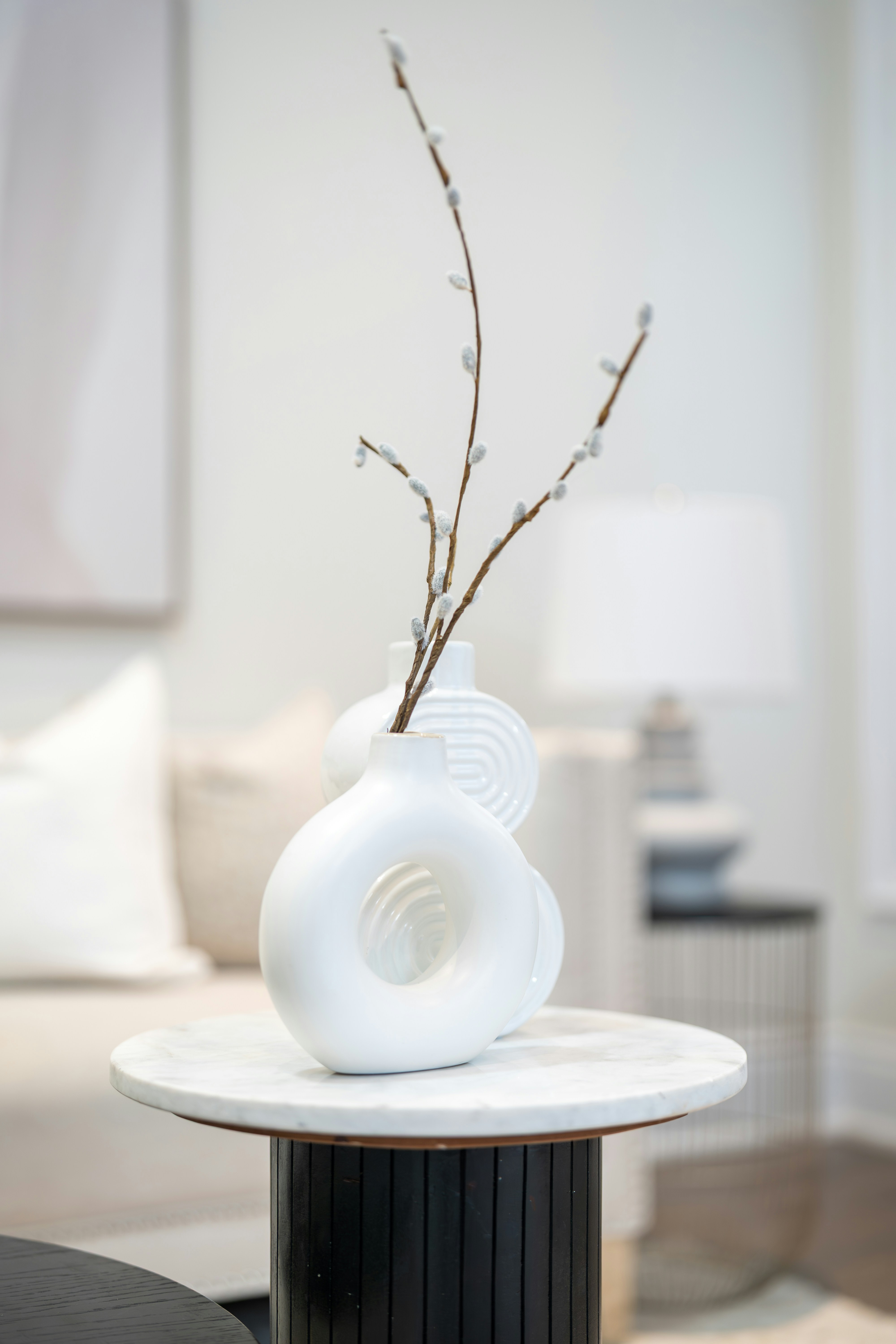 White ceramic vase with branch arrangement on a marble-topped table in a bright living room