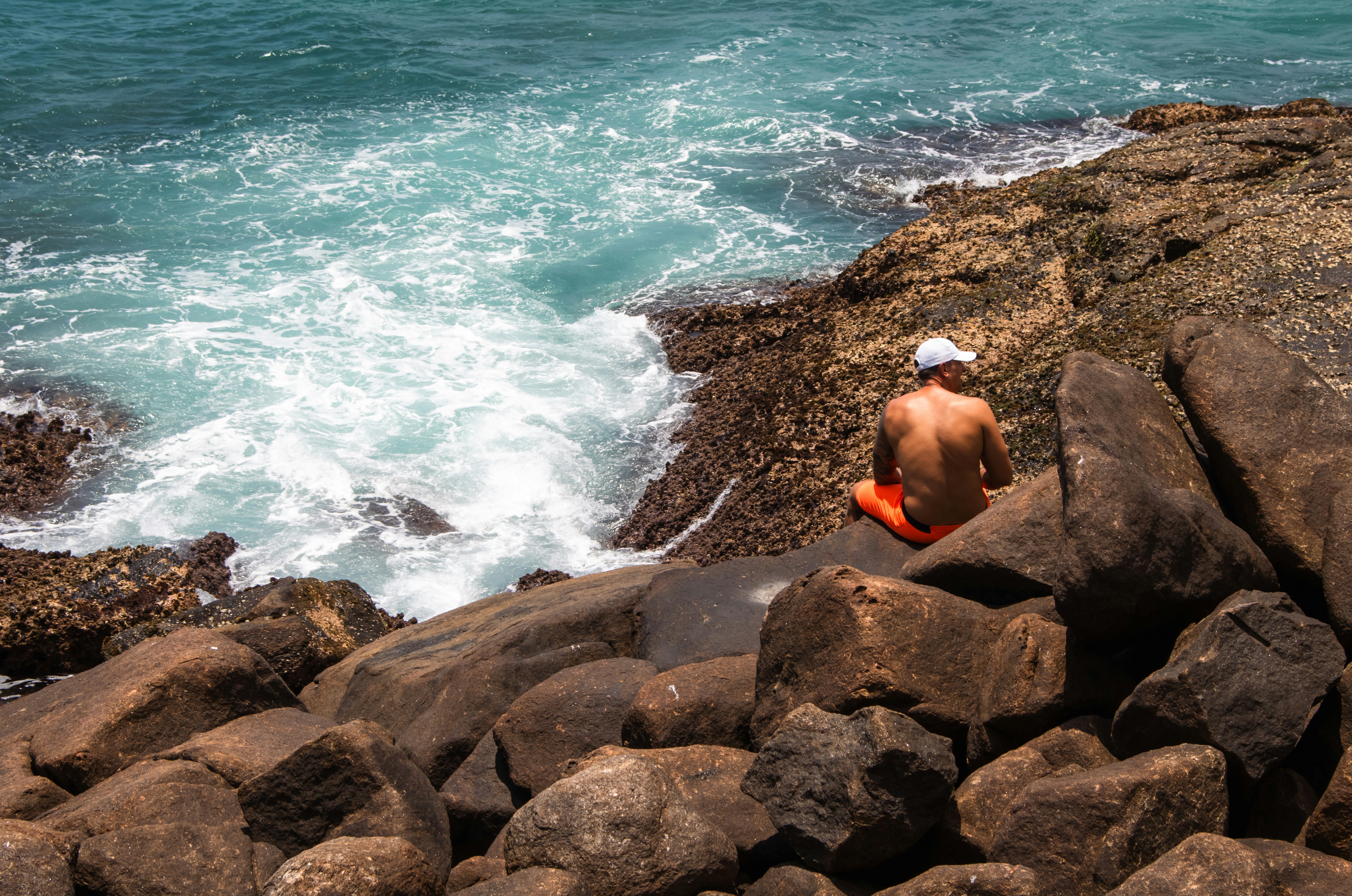 Solitary Figure on Weathered Rocks Beneath a Turquoise Tide