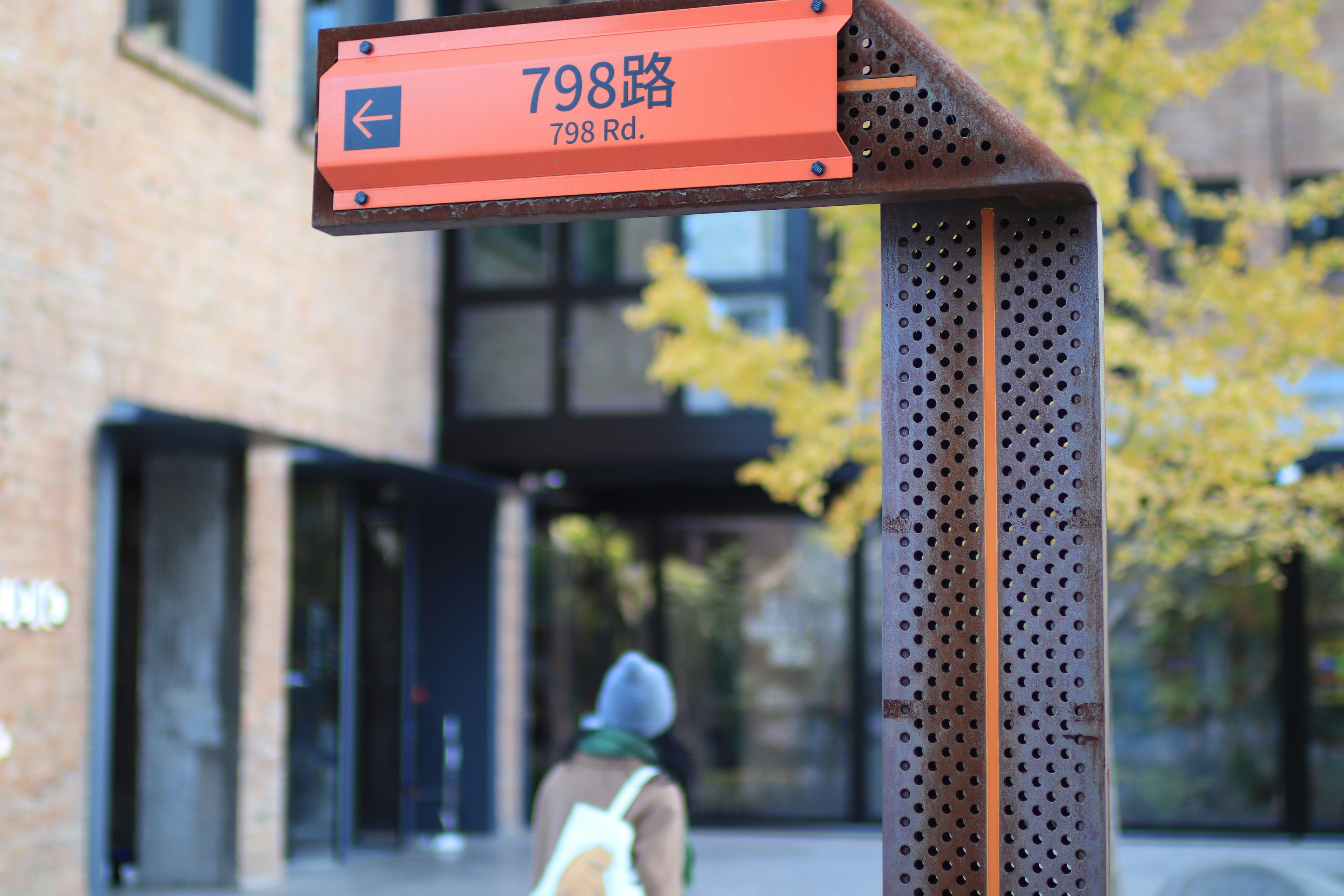 Street Sign Over a Perforated Post Framing an Out-of-Focus Pedestrian