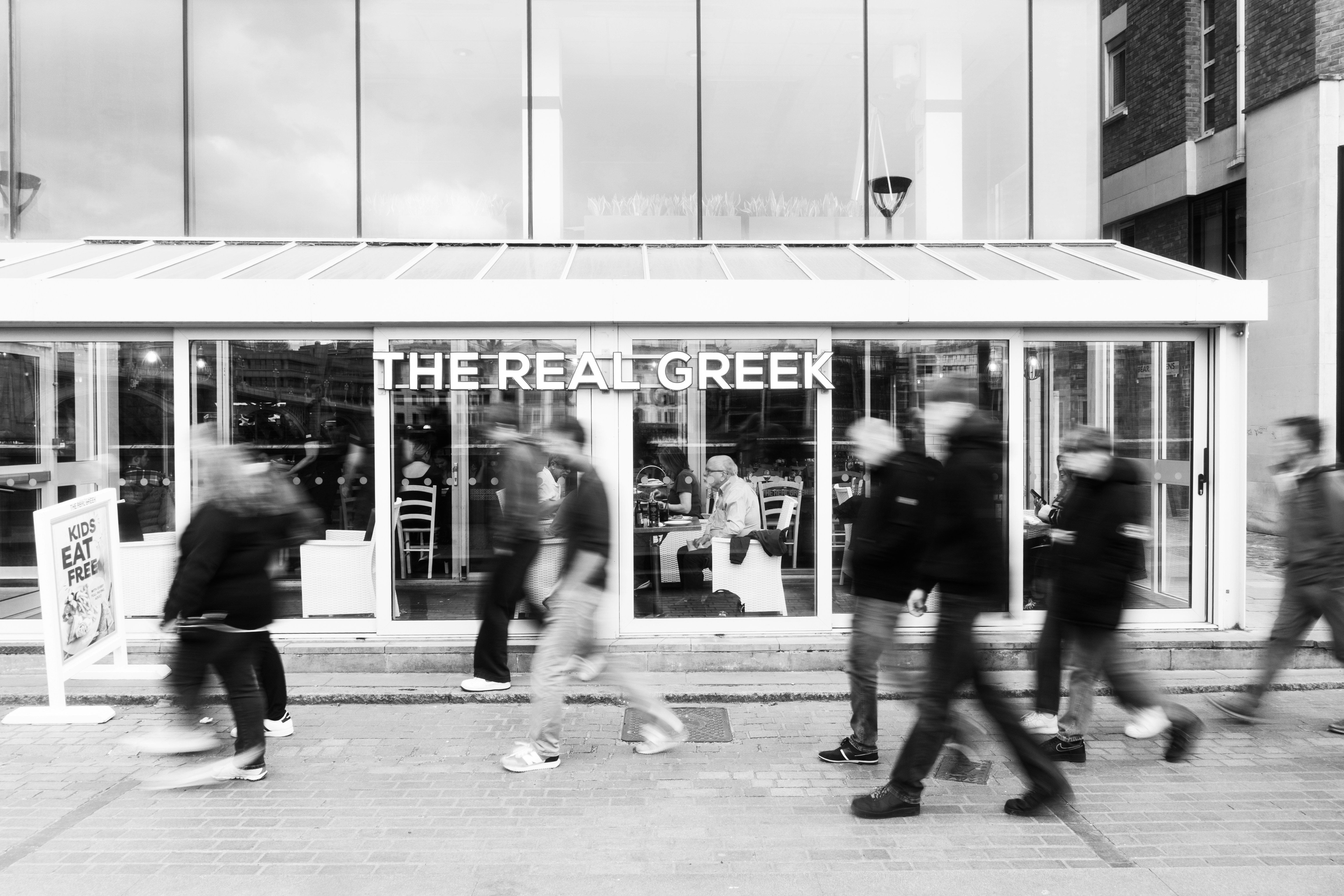Pedestrians in motion around a monochrome cafe storefront
