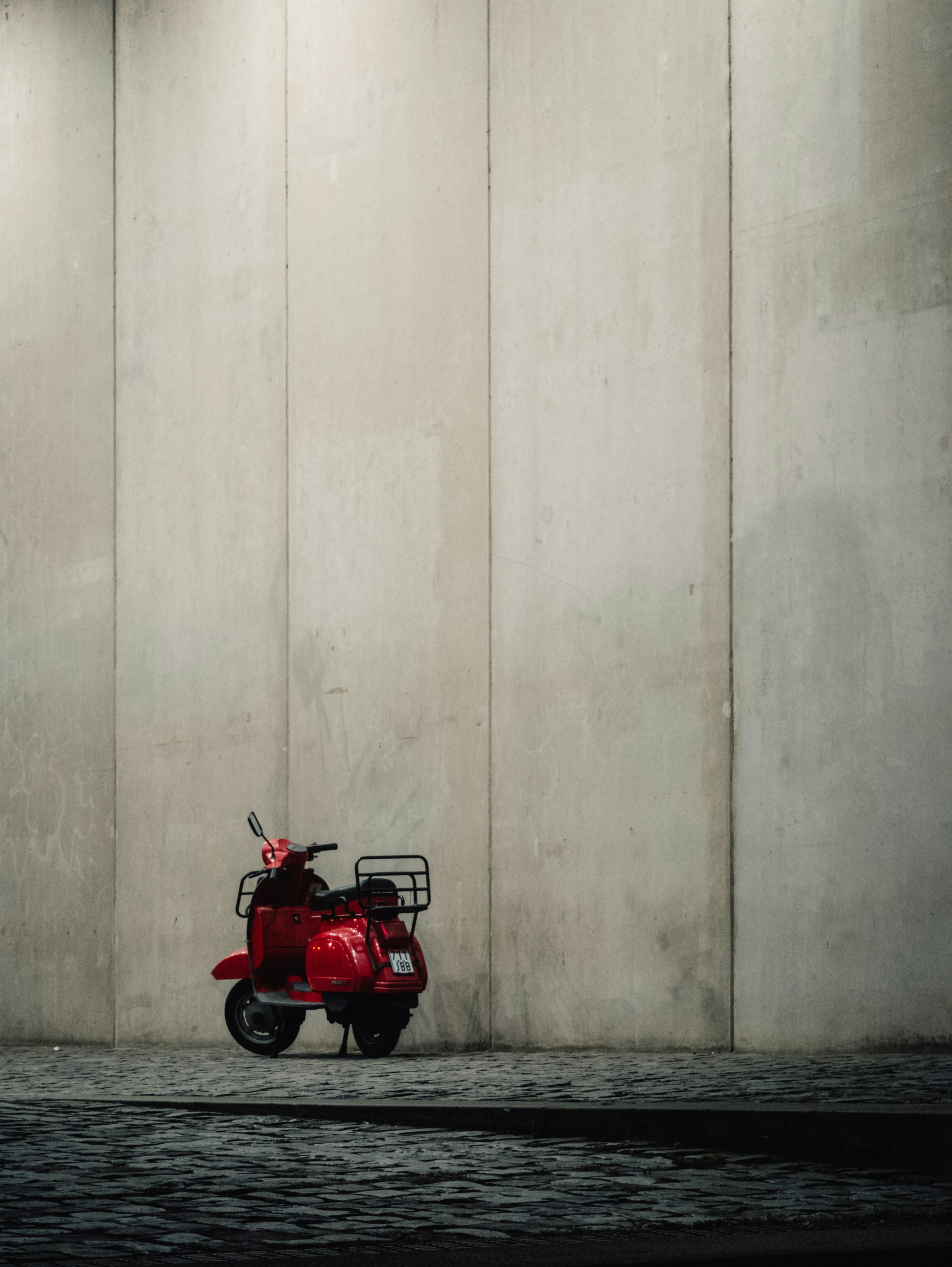 Red Vespa Quietly Anchored Against a Monolithic Wall