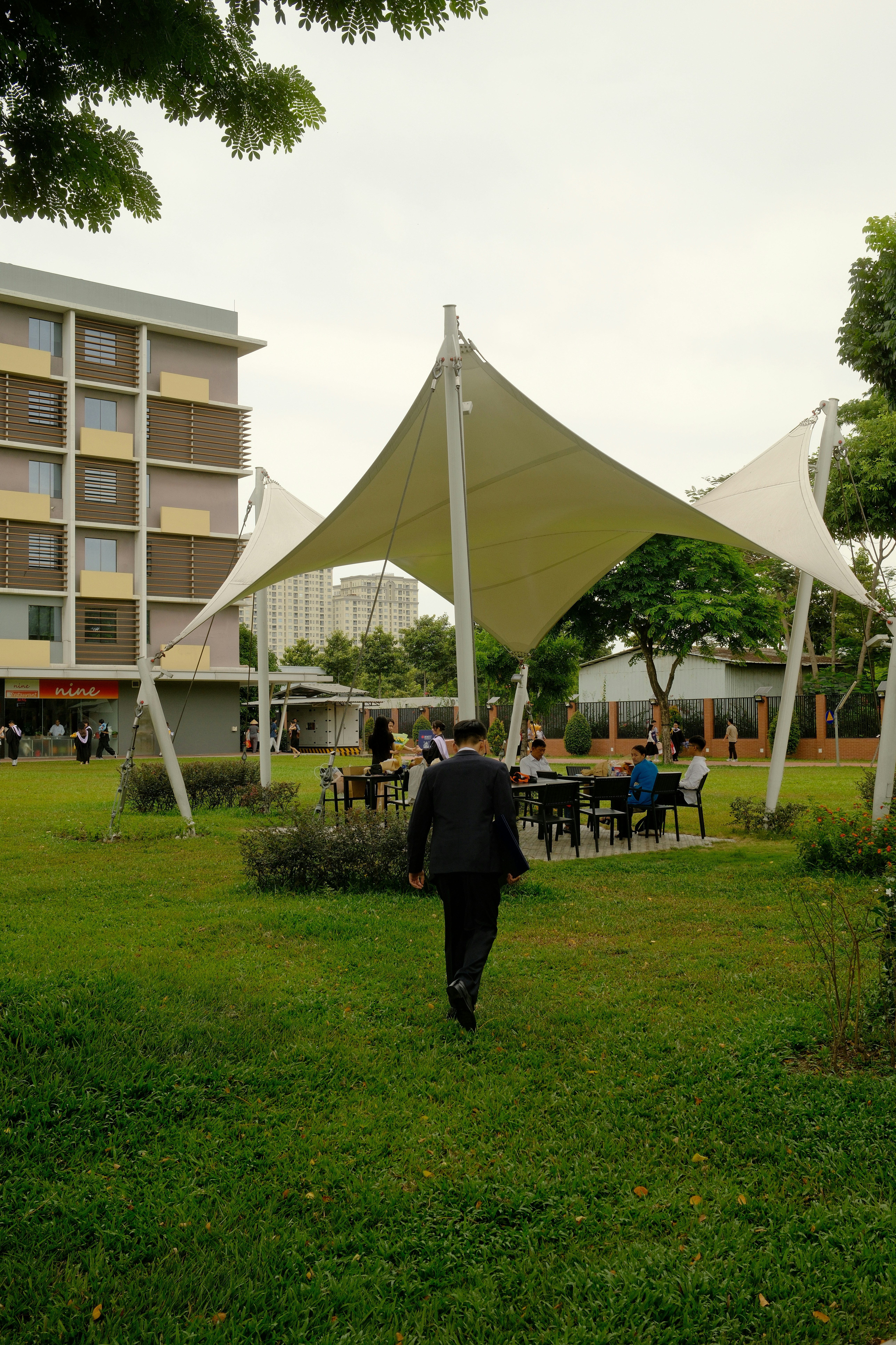 Office worker strides toward a shaded gathering under modern tensile structures