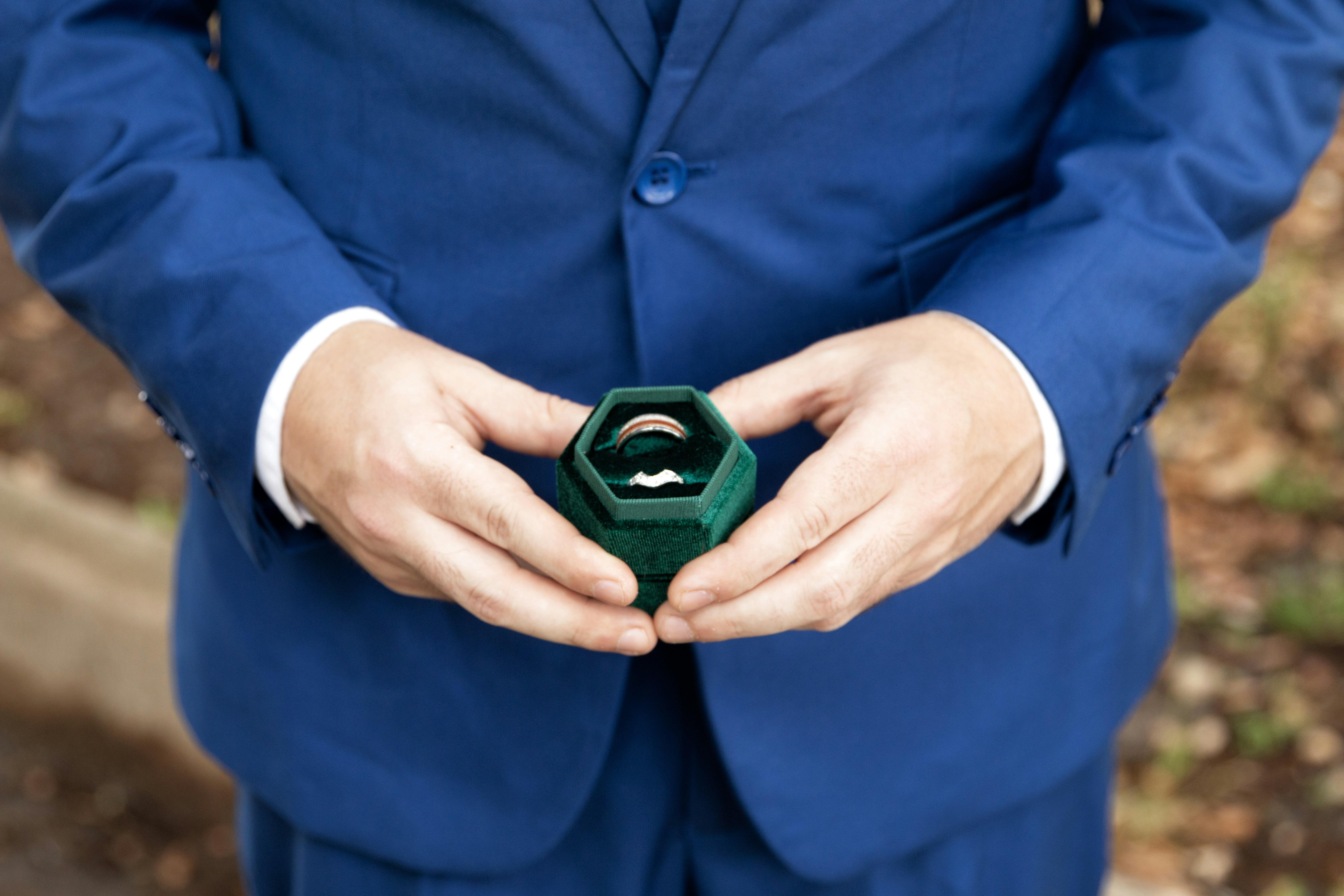 Blue-suited hands cradle a distinctive hexagonal ring box