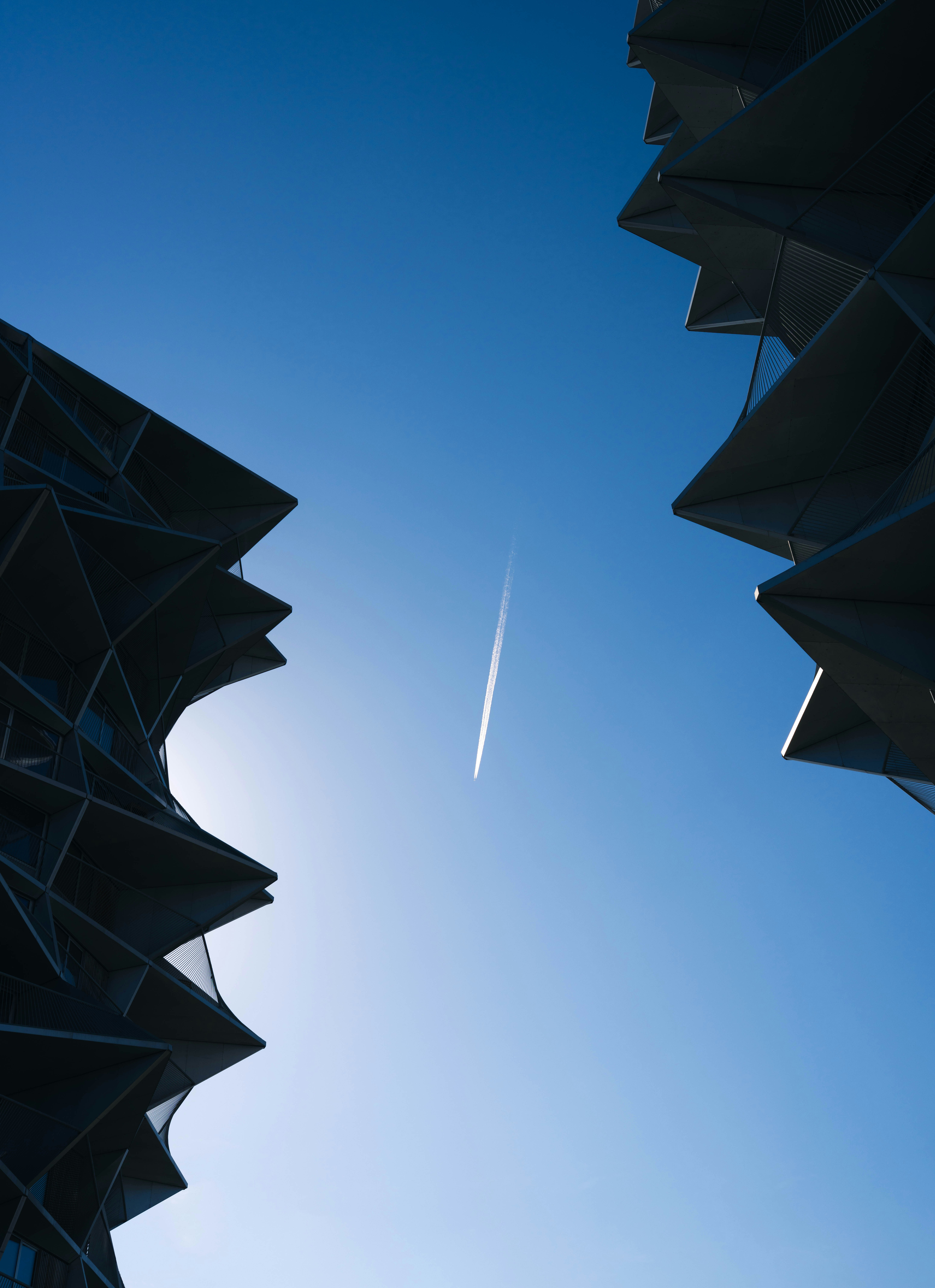 Skyward Convergence: A Jet Contrail Between Architectural Peaks