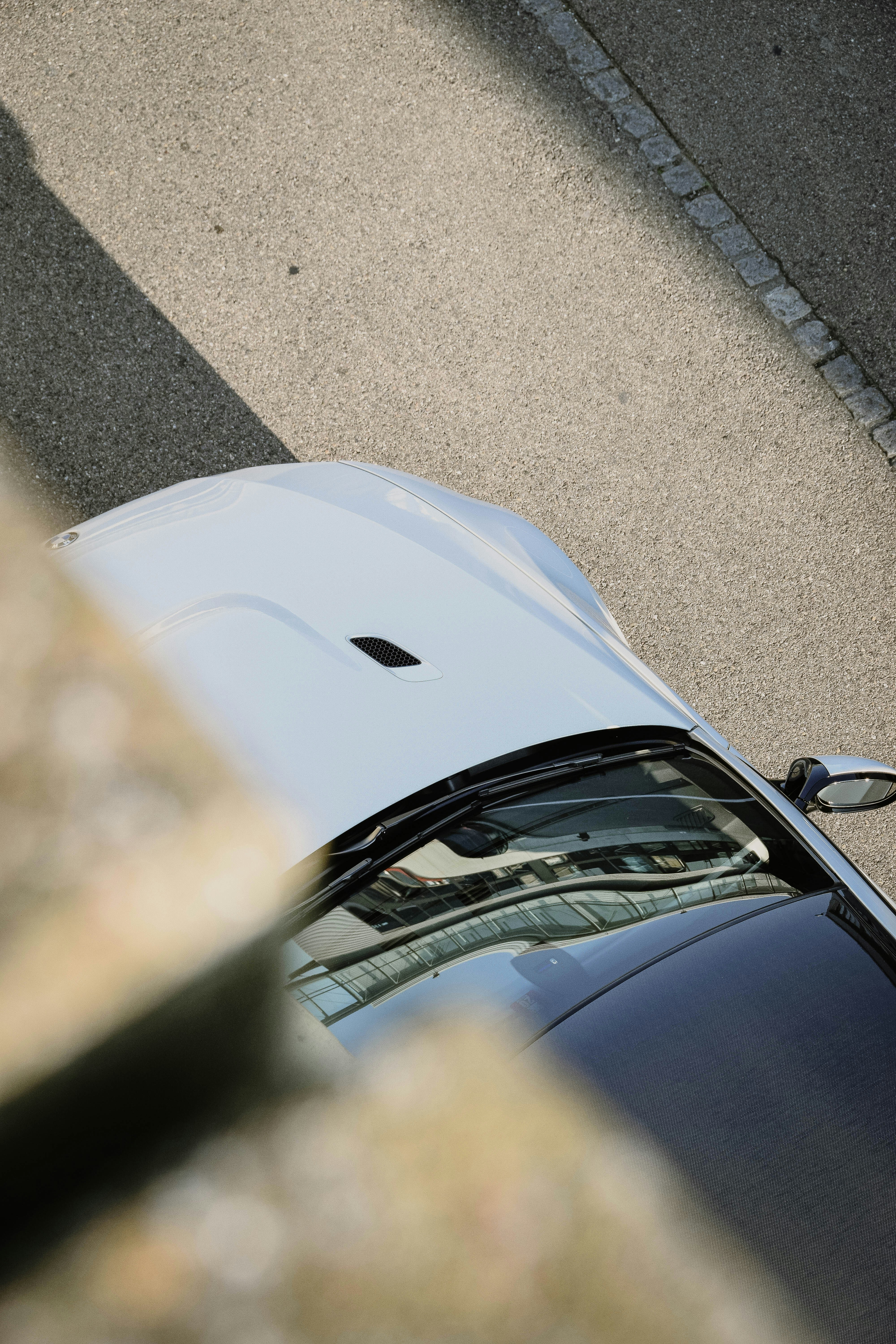 A tilted silver car seen from above the curb, with street and window reflections