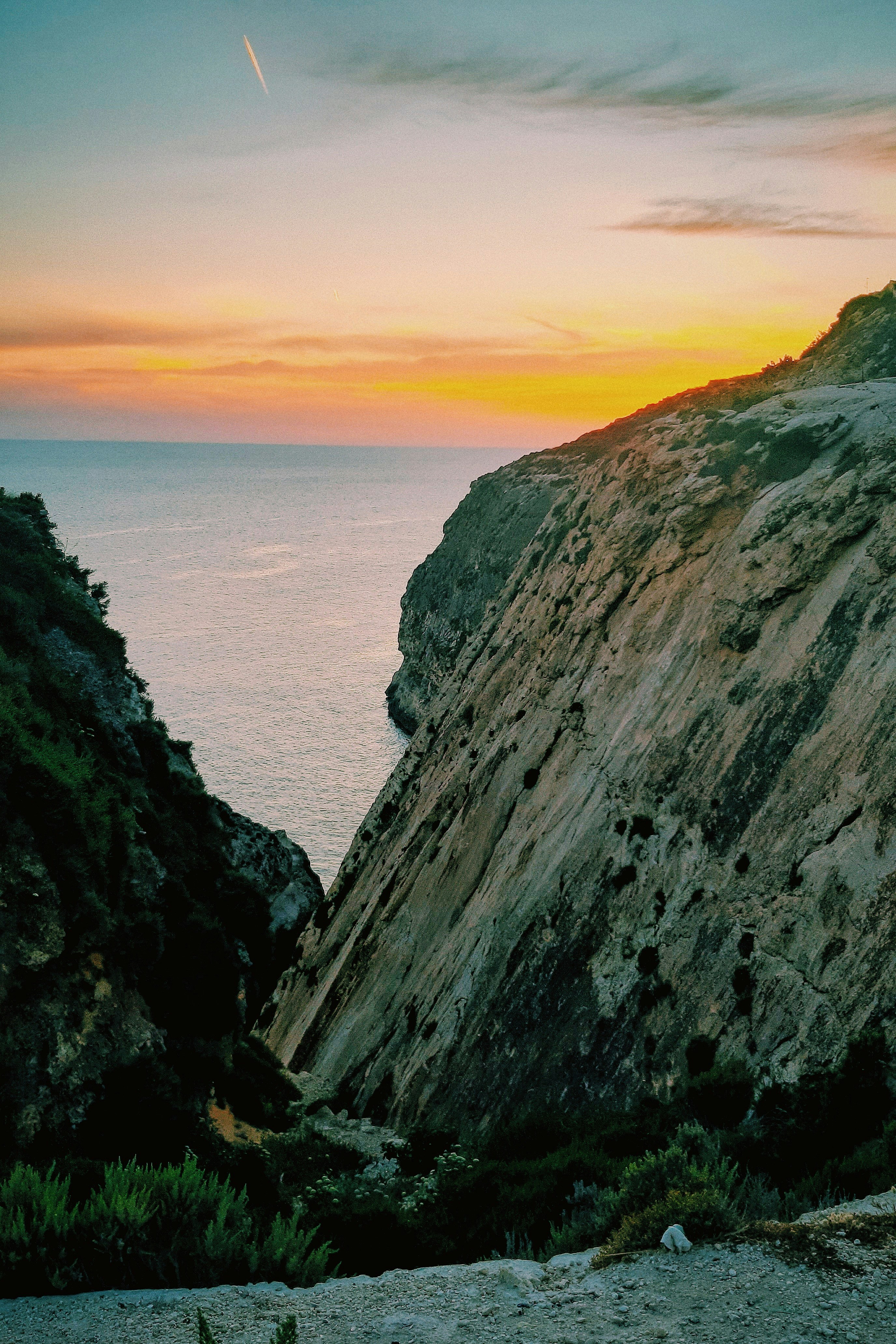 Dramatic coastal canyon at sunset with the sea beyond, cliff faces framing the scene.