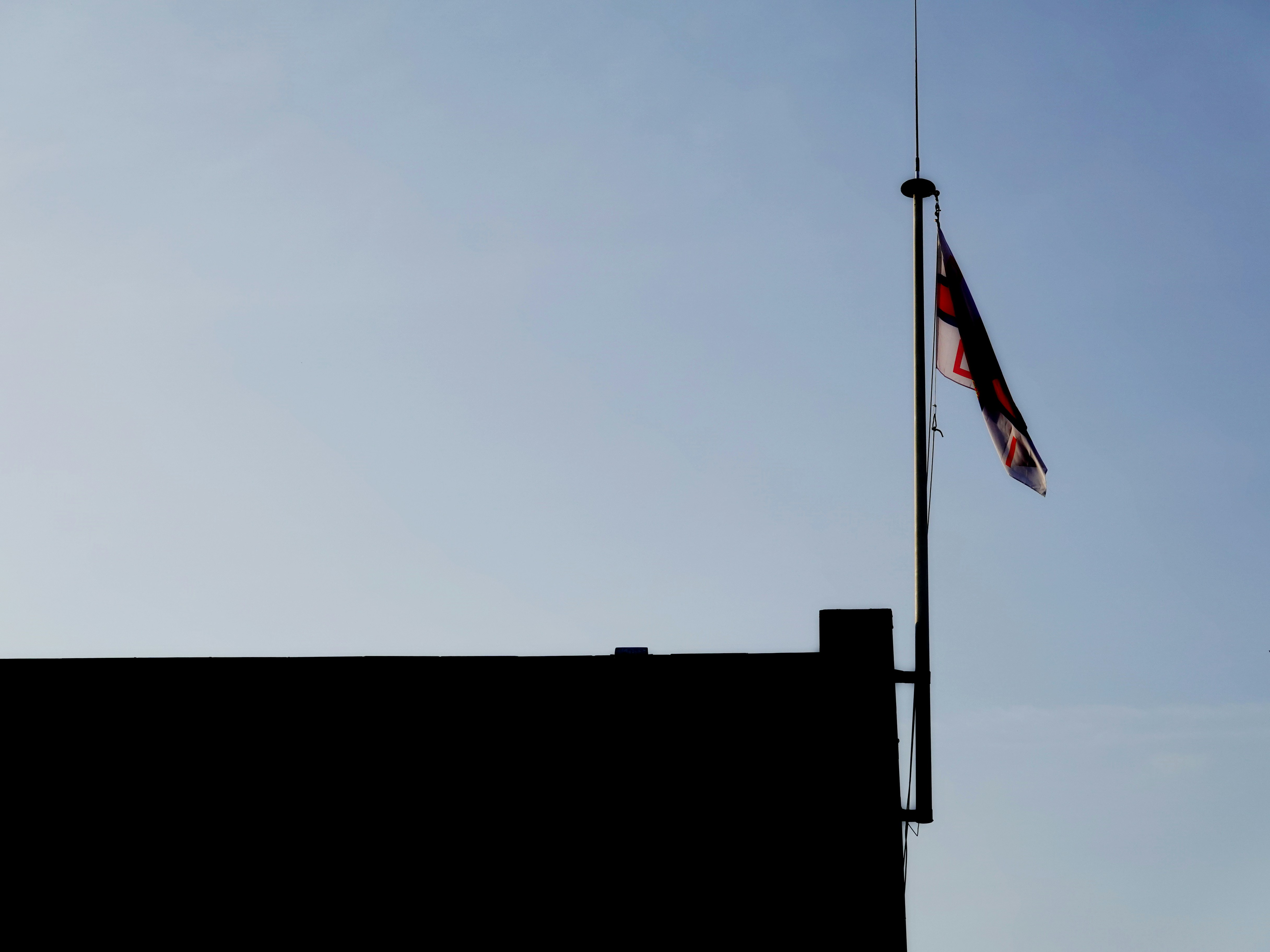 Flag atop a silhouette: a quiet facade under a clear sky