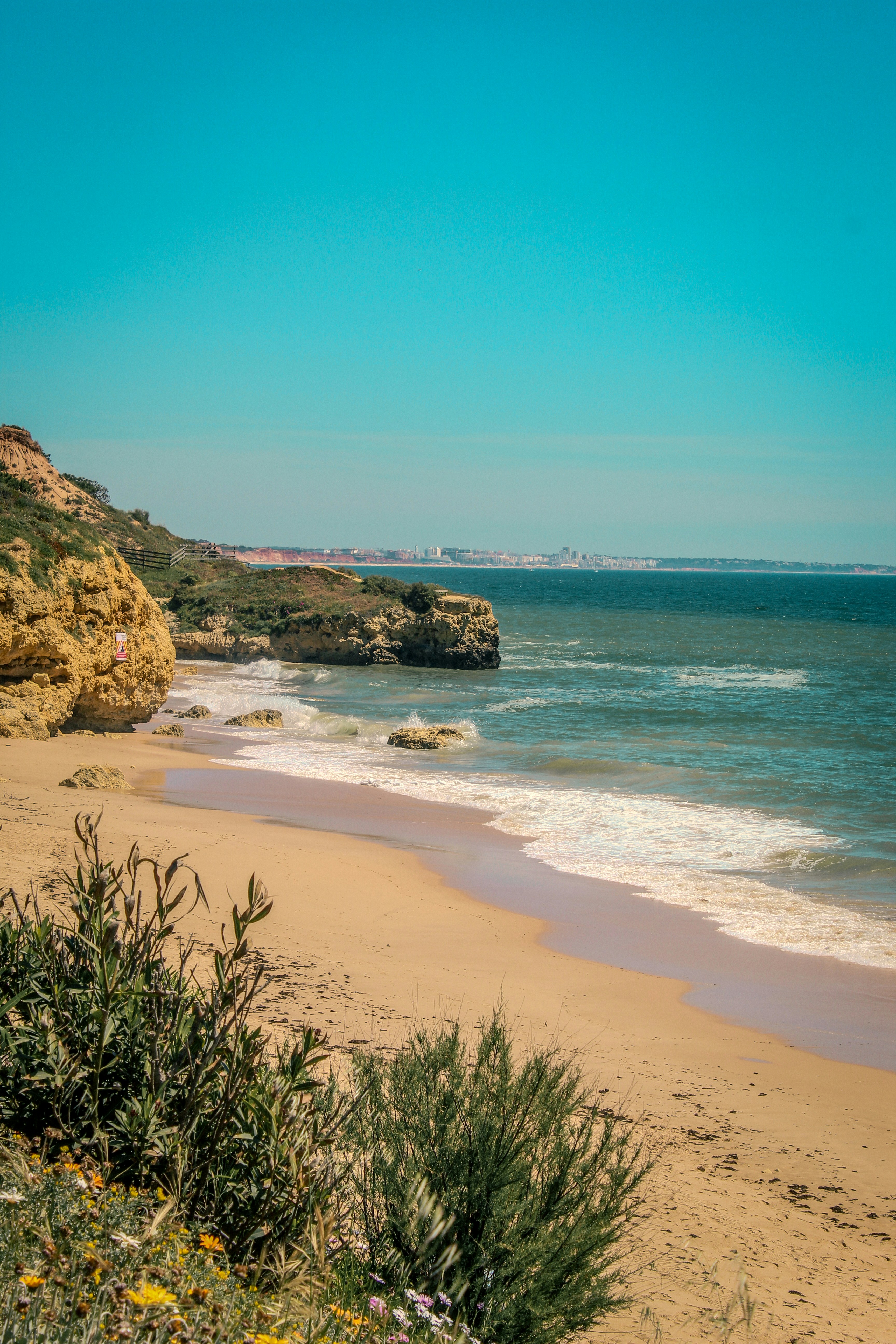 Sandy beach with rocky cliffs and blue ocean.
