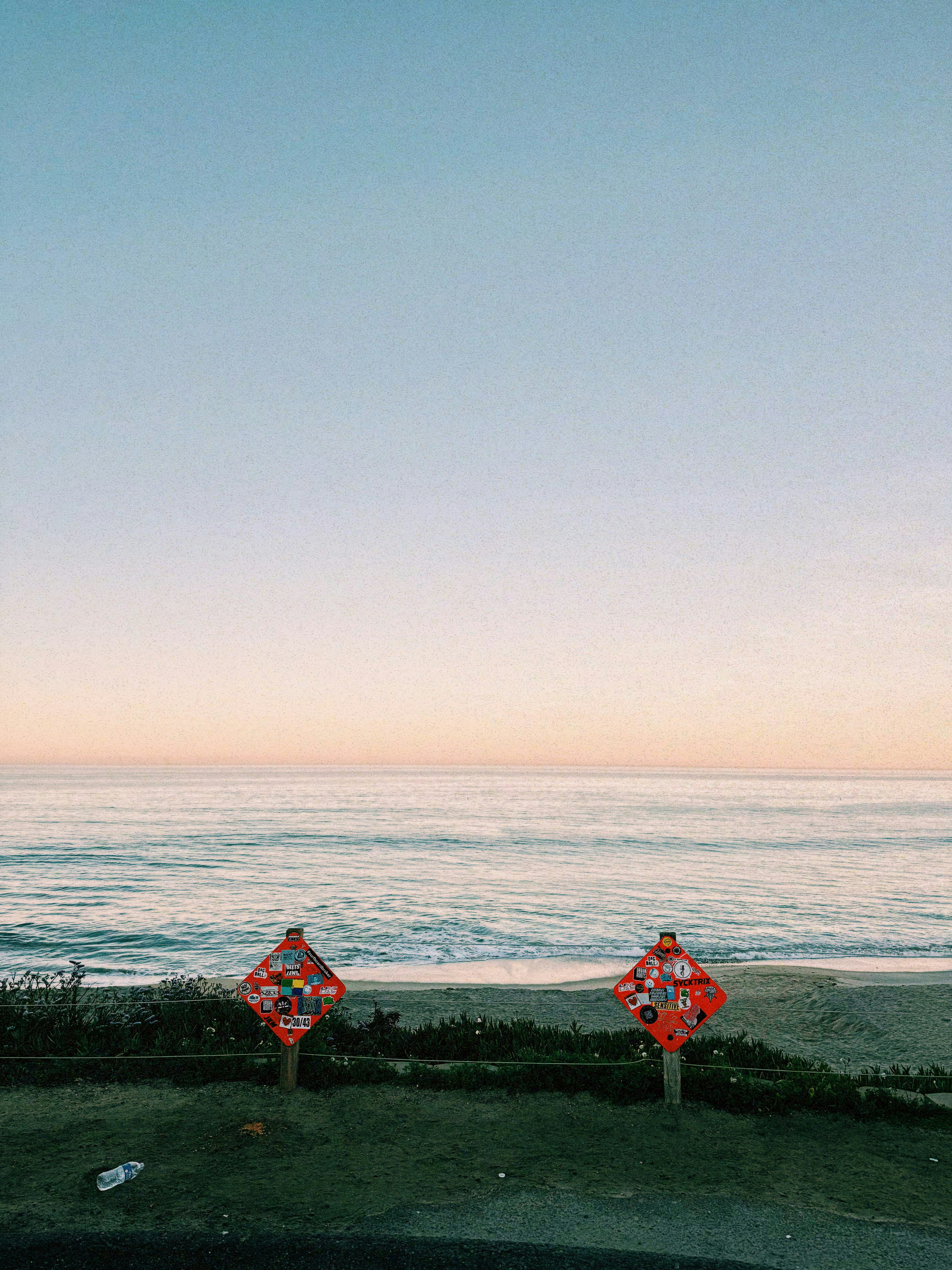 Two red signs on a seaside fence at sunset