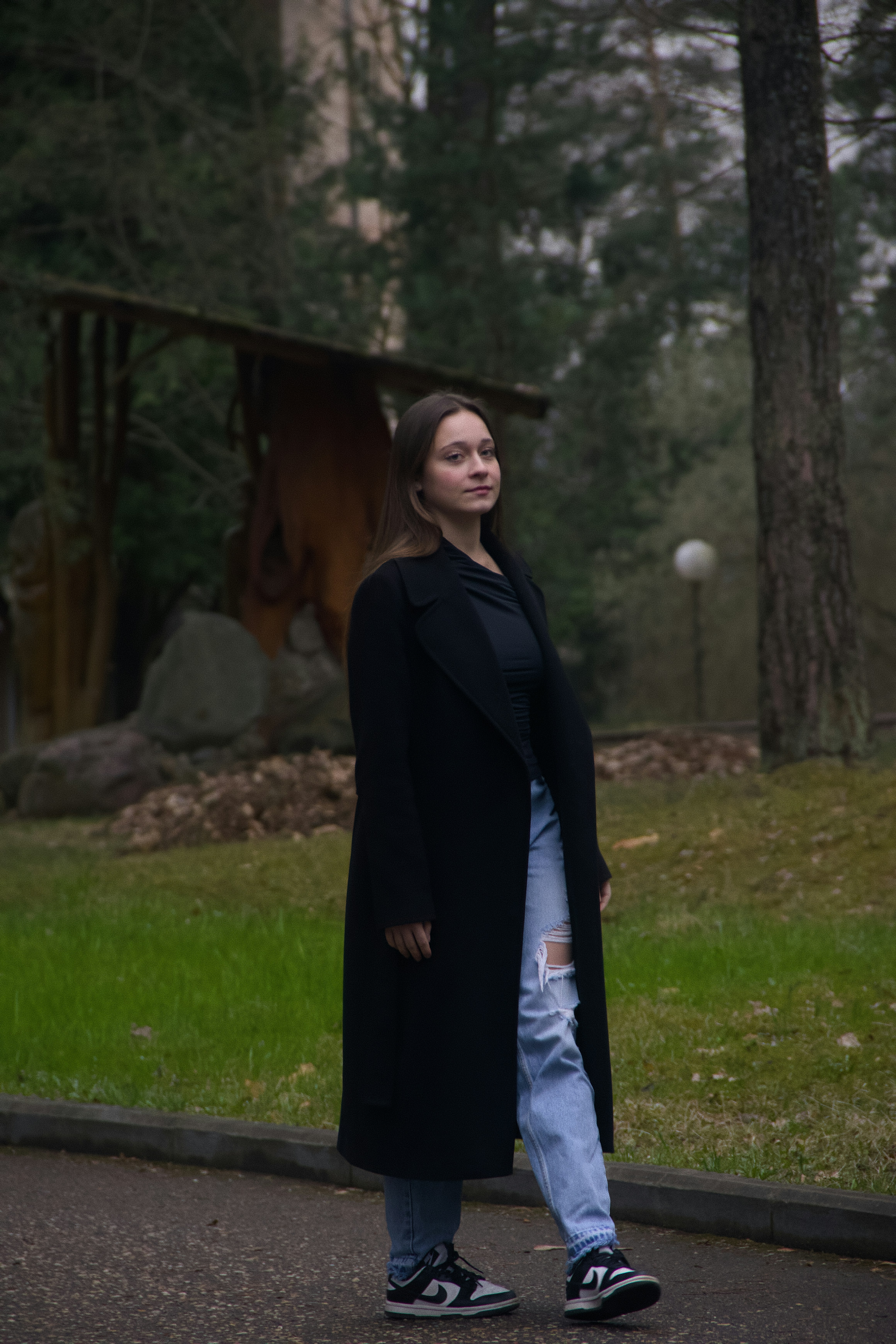 Hushed Portrait in the Woods: A Woman in a Long Coat Beside a Quiet Path