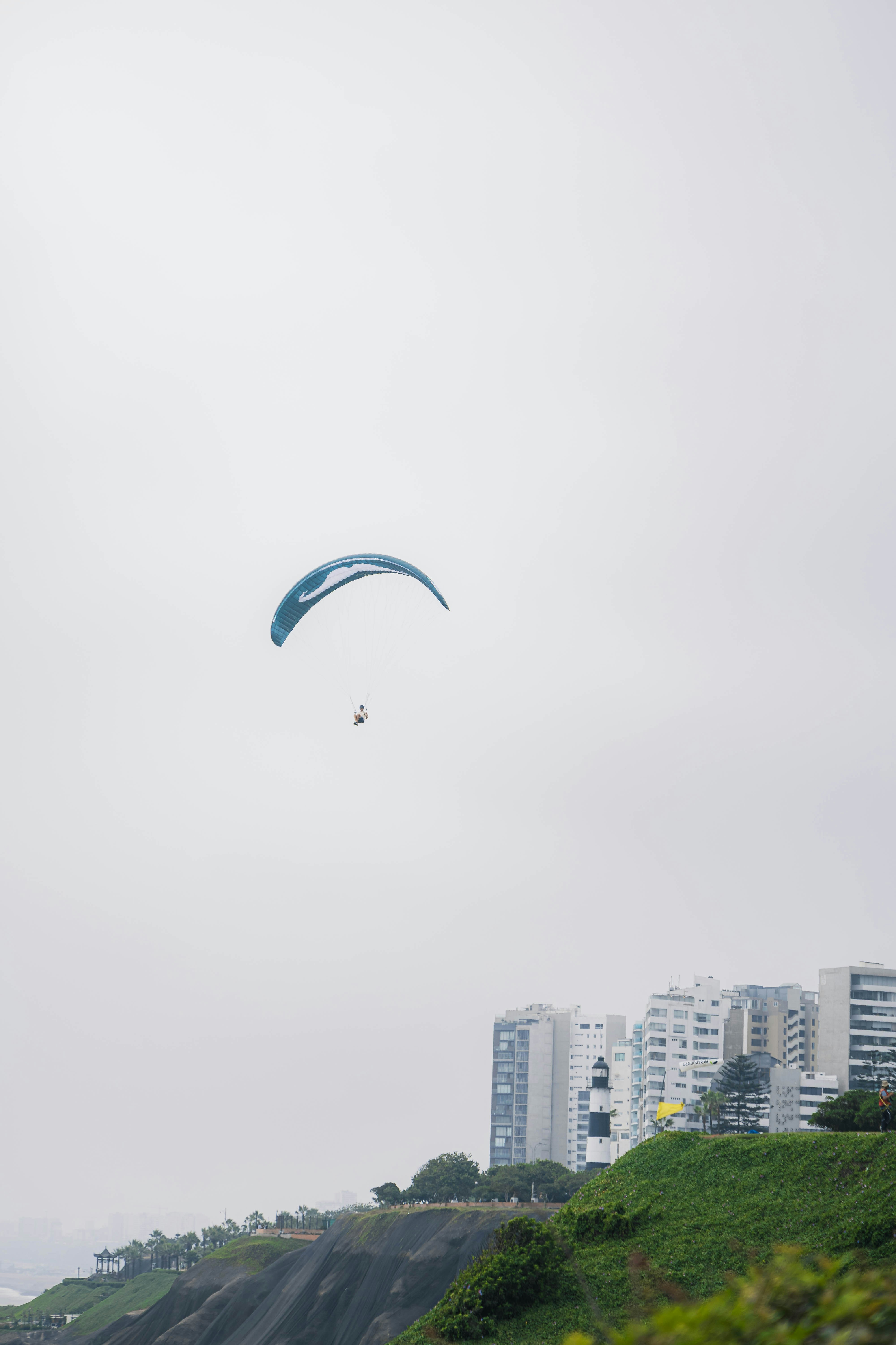 Blue Paraglider Above Coastal Cliffs and Cityscape