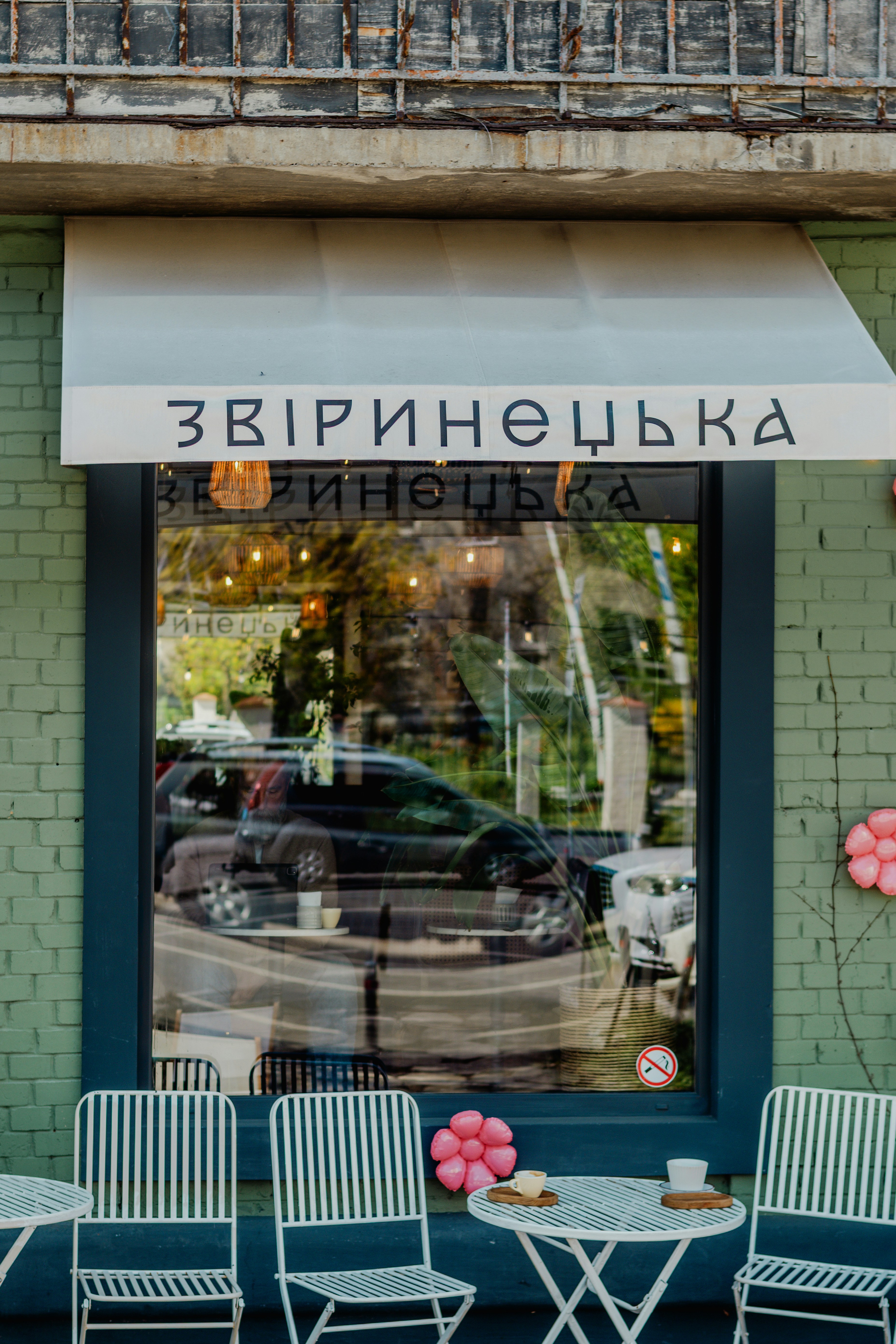 Green storefront, soft pastel café chairs, and a sunlit awning