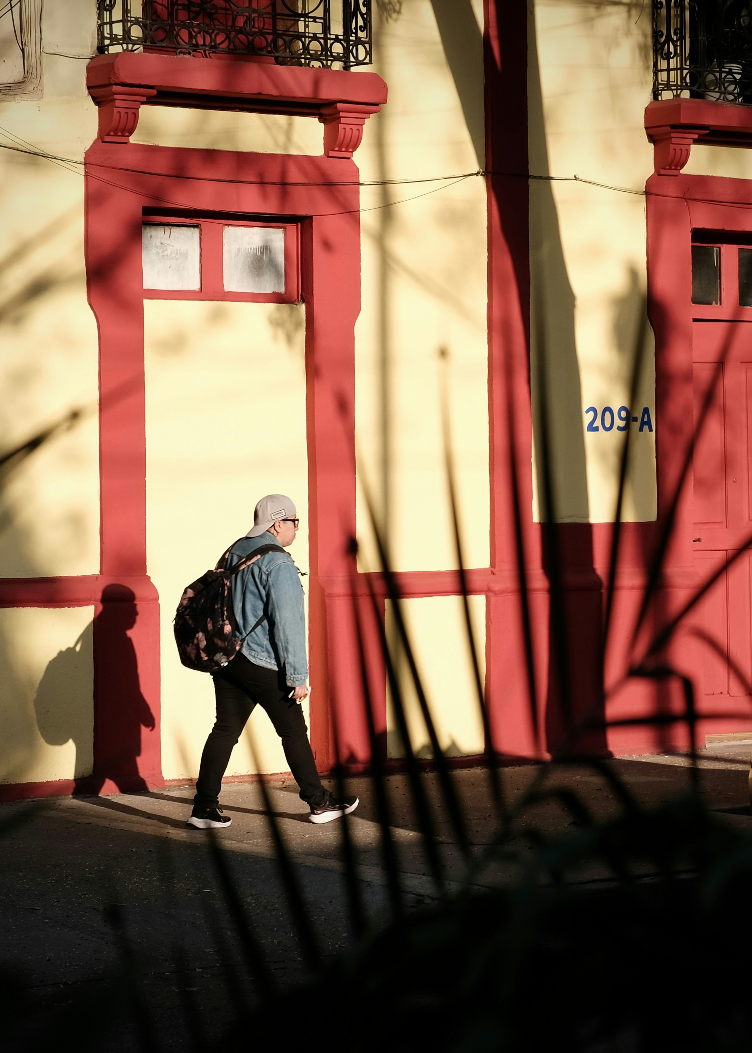 Striding Past a Bold Facade: A Quiet Portrait in Red and Yellow