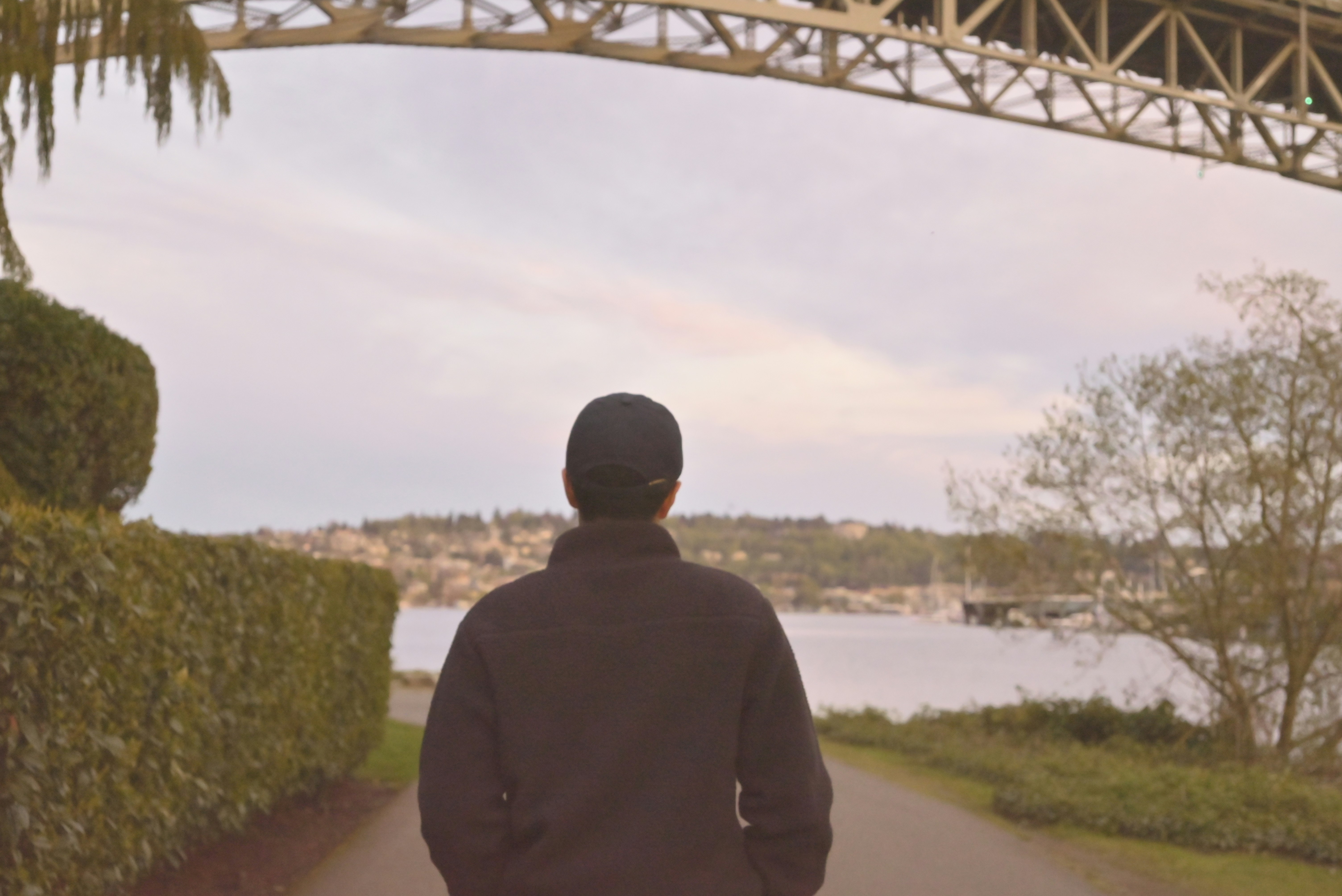 Man in a dark jacket walking toward a scenic lake under a bridge