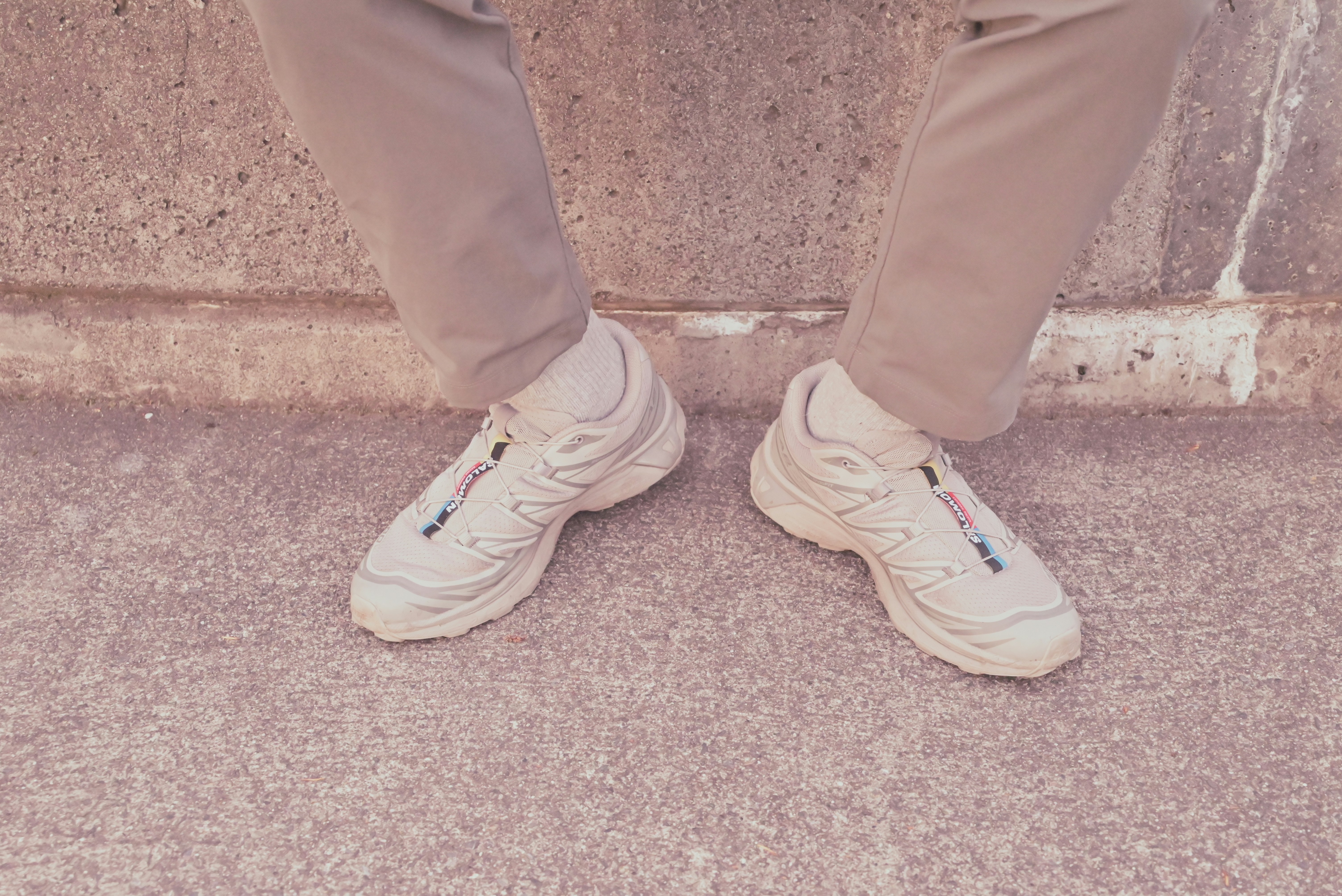 Grounded Steps: Sneakers and Beige Trousers at the Edge of a Wall